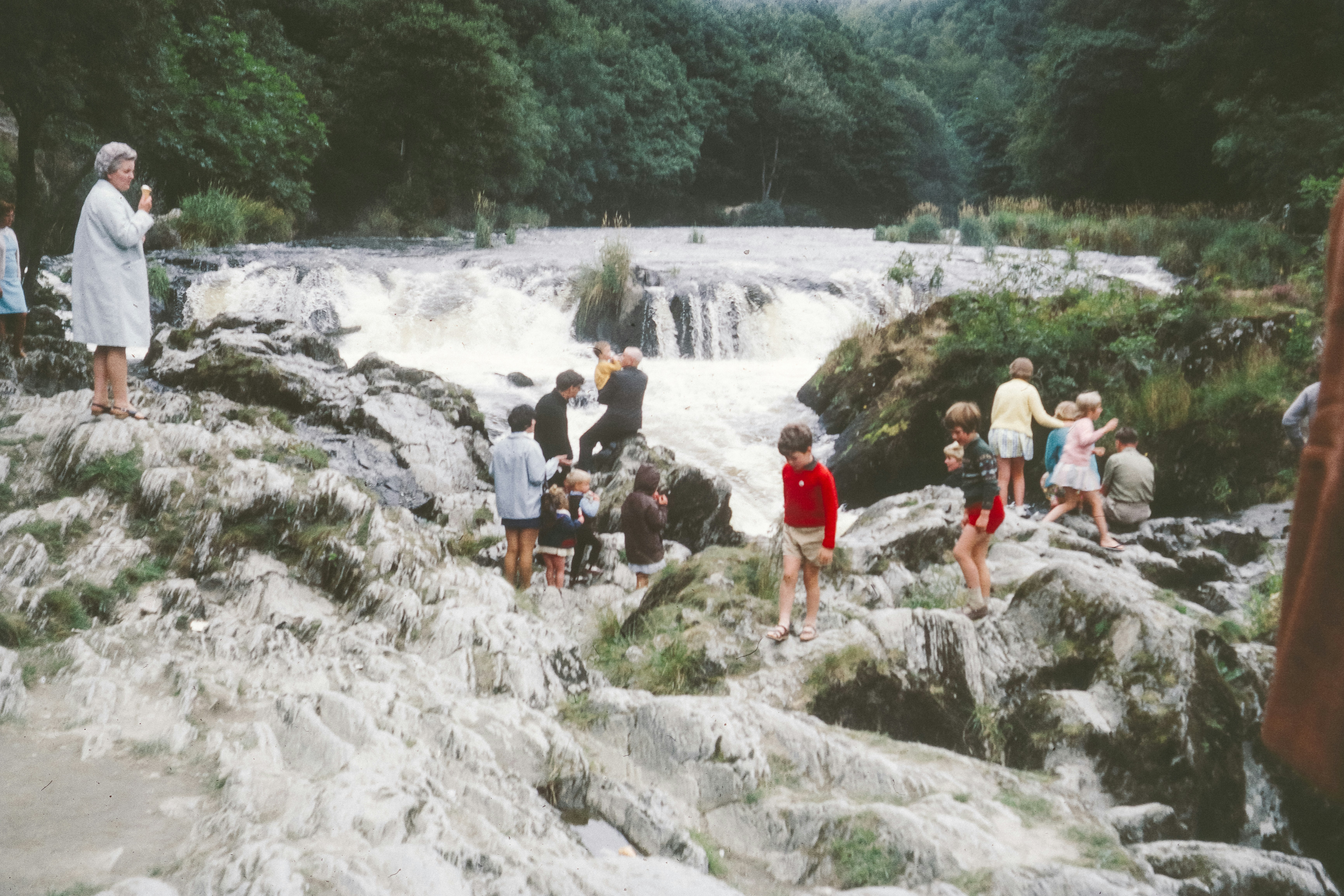 Children explore a rocky riverbank under a park waterfall