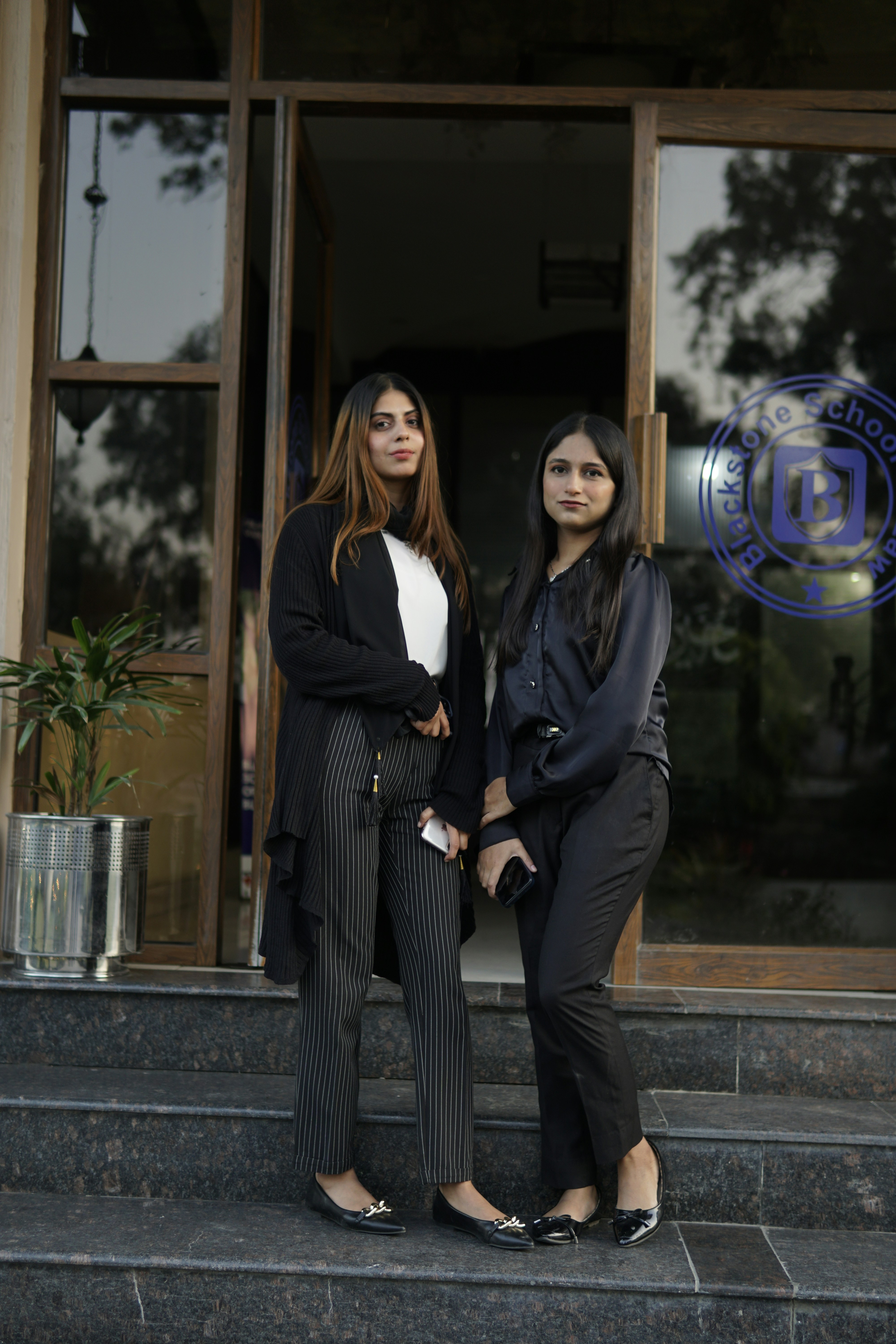 Two women on the steps of a modern building, confidence in monochrome outfits