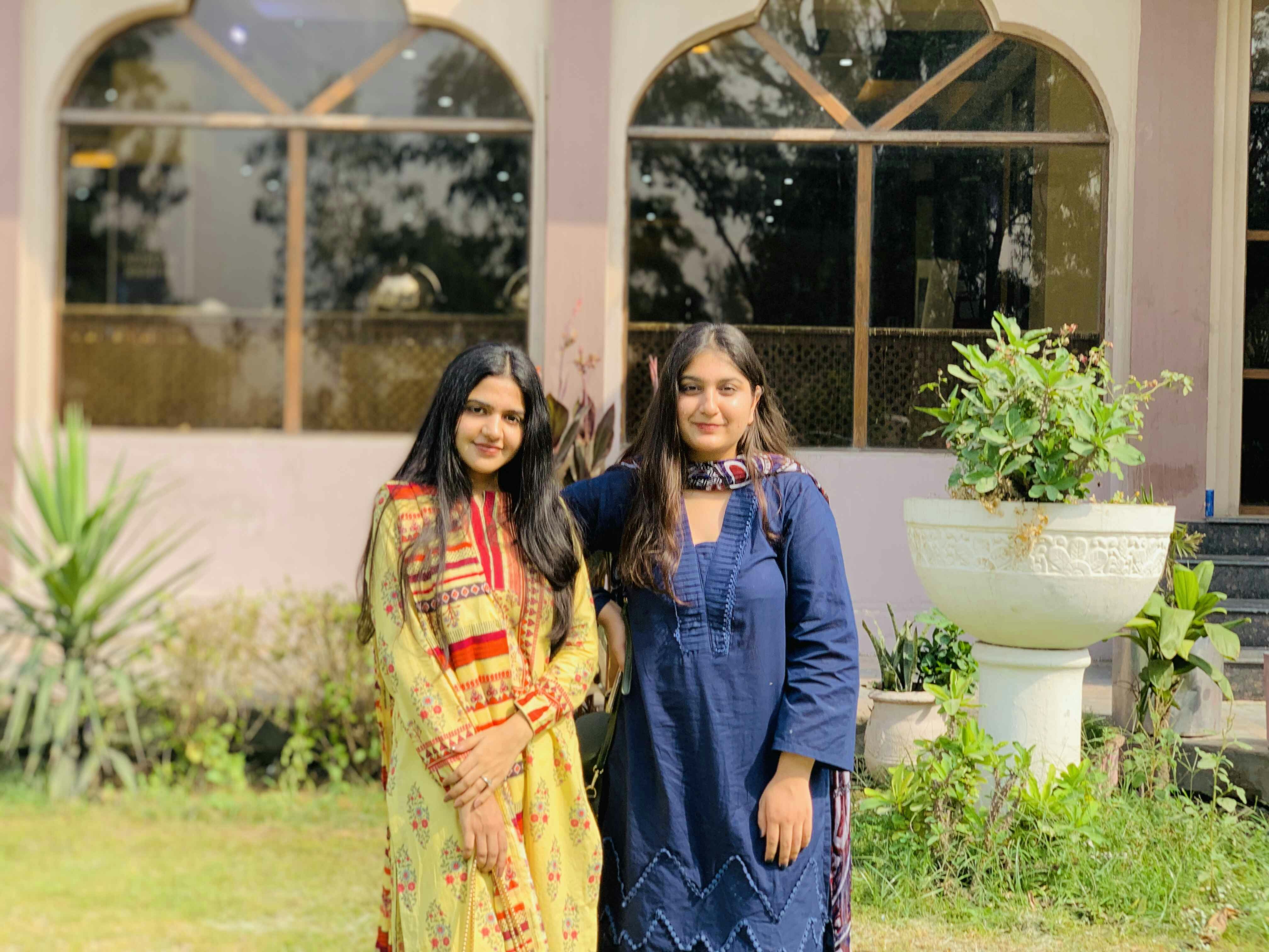 Two smiling women stand outside a building.
