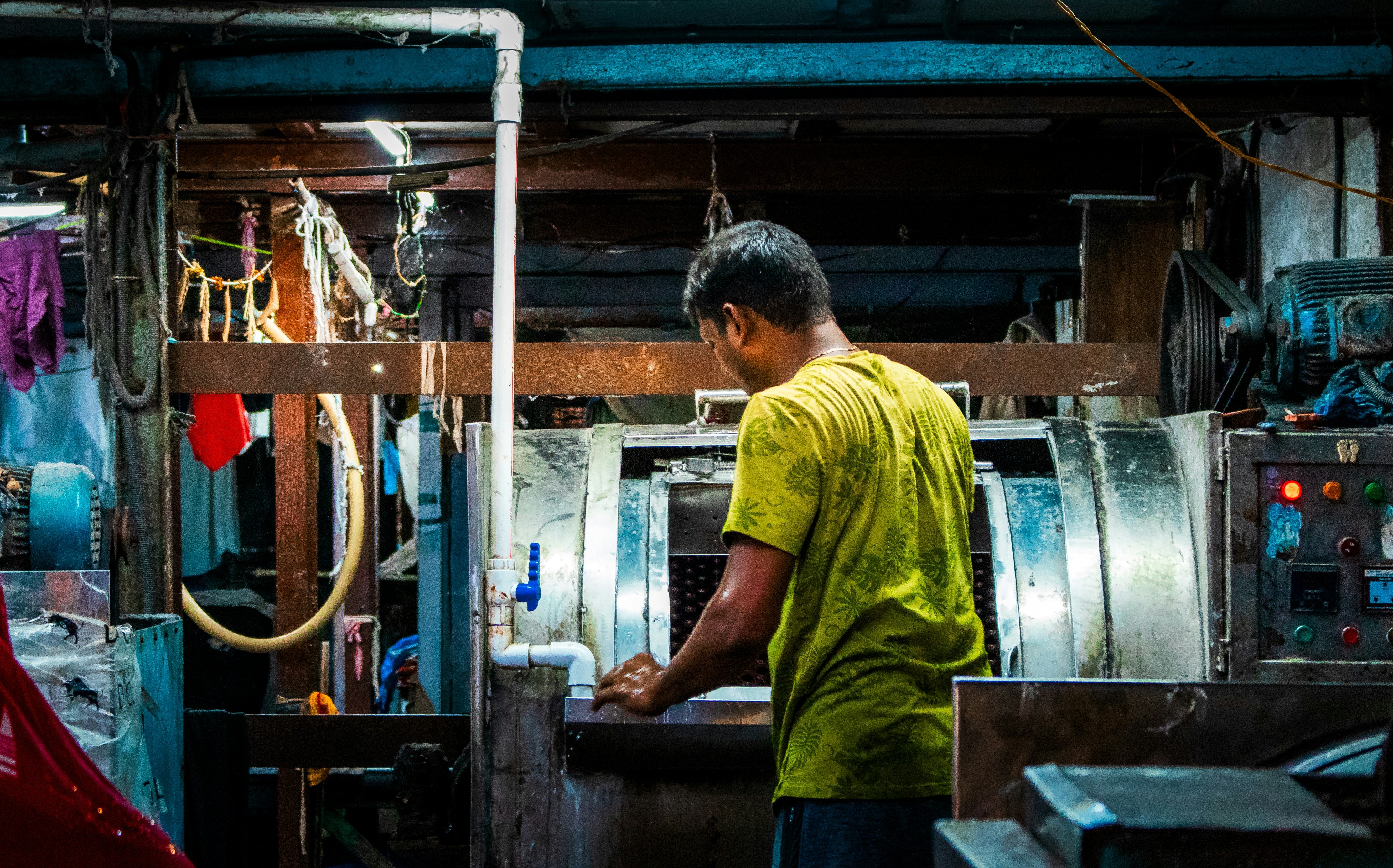 A worker loading clothes into an industrial washing drum inside Dhobi Ghat in Mumbai. It is suitable for use in articles, presentations, research on informal economies, and visual documentation of workplace environments in India.