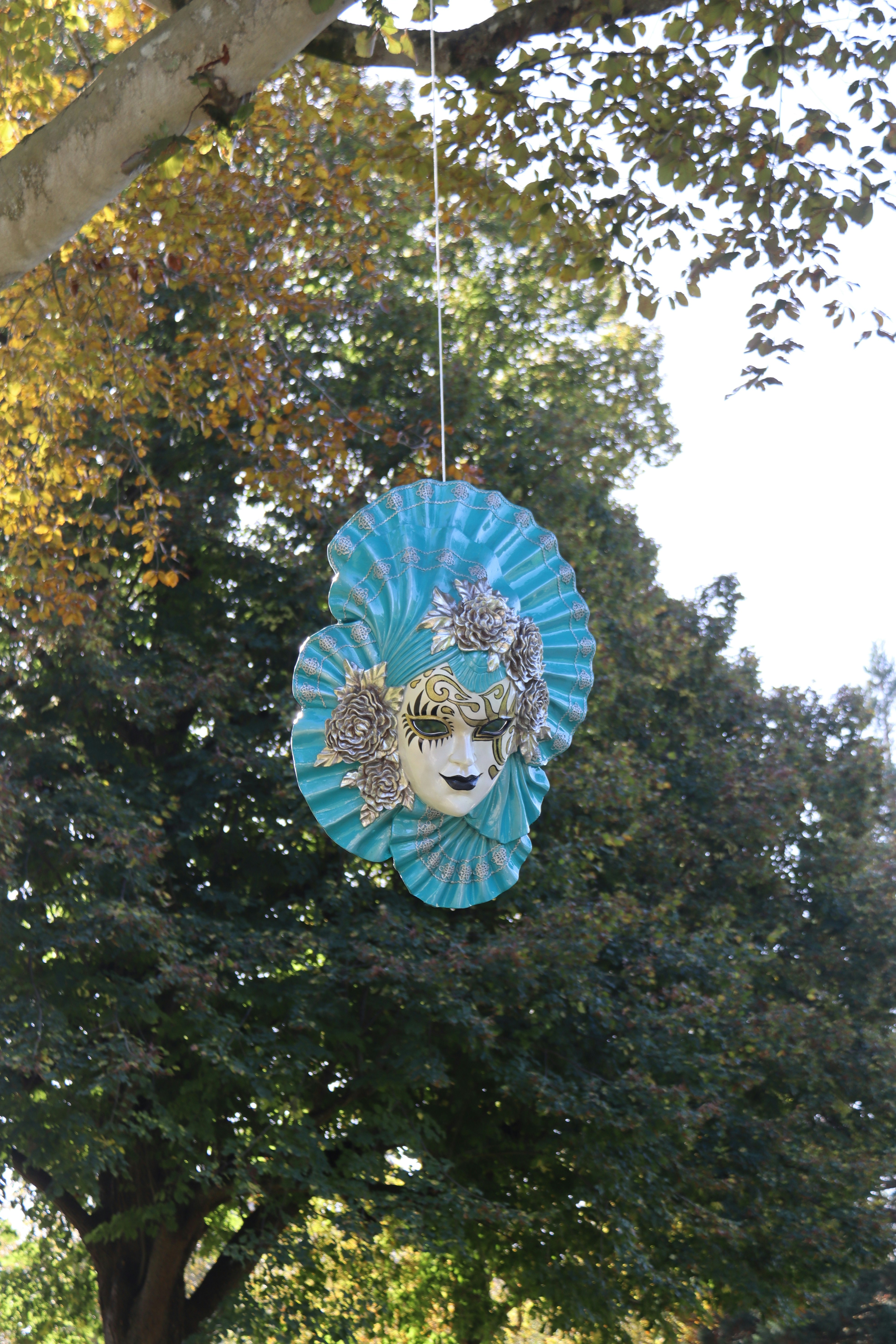Floating Theater: A Blue Mask Ornament Dangles Against Sunlit Foliage