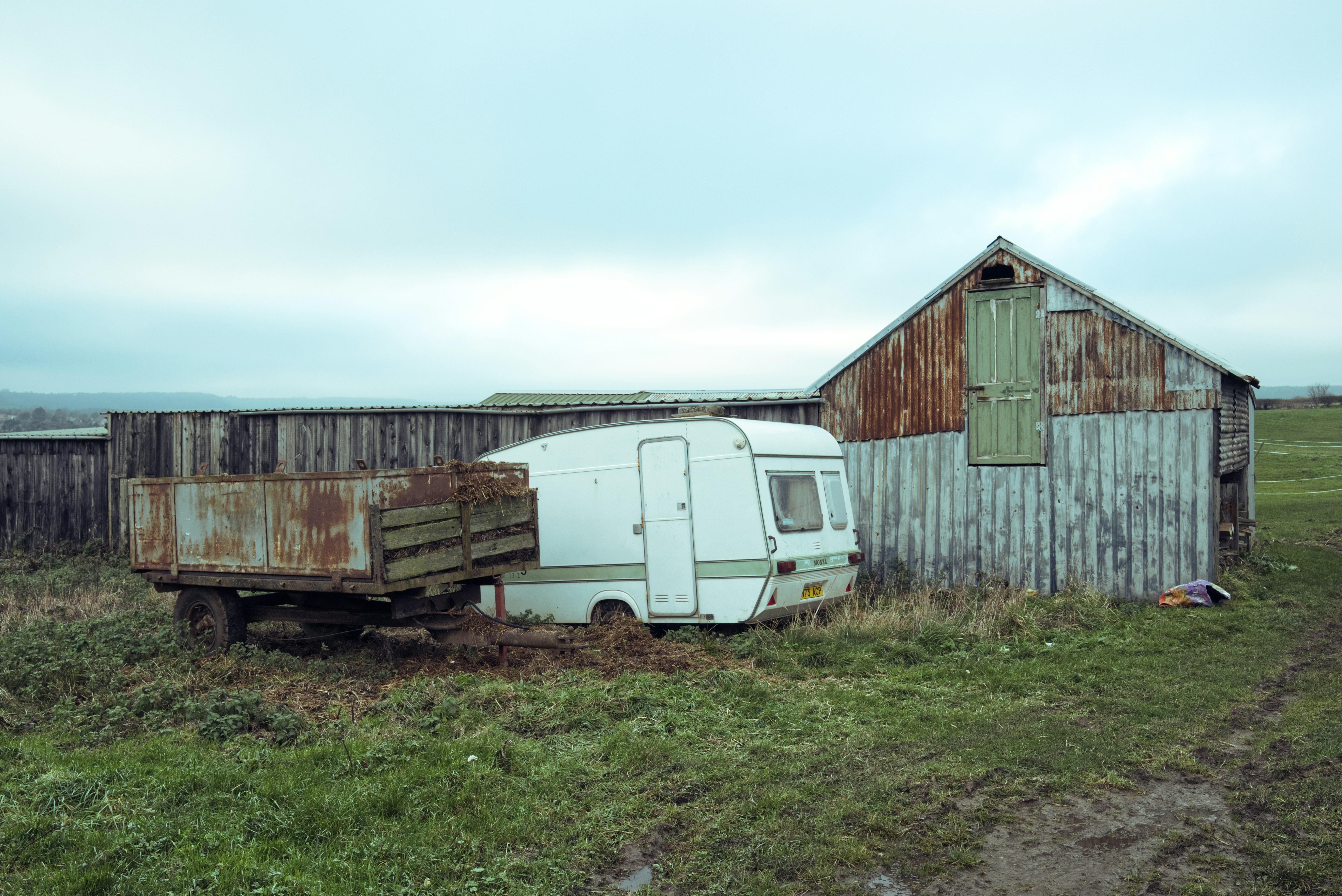 Weathered caravan and rusted trailer beside a weathered shed