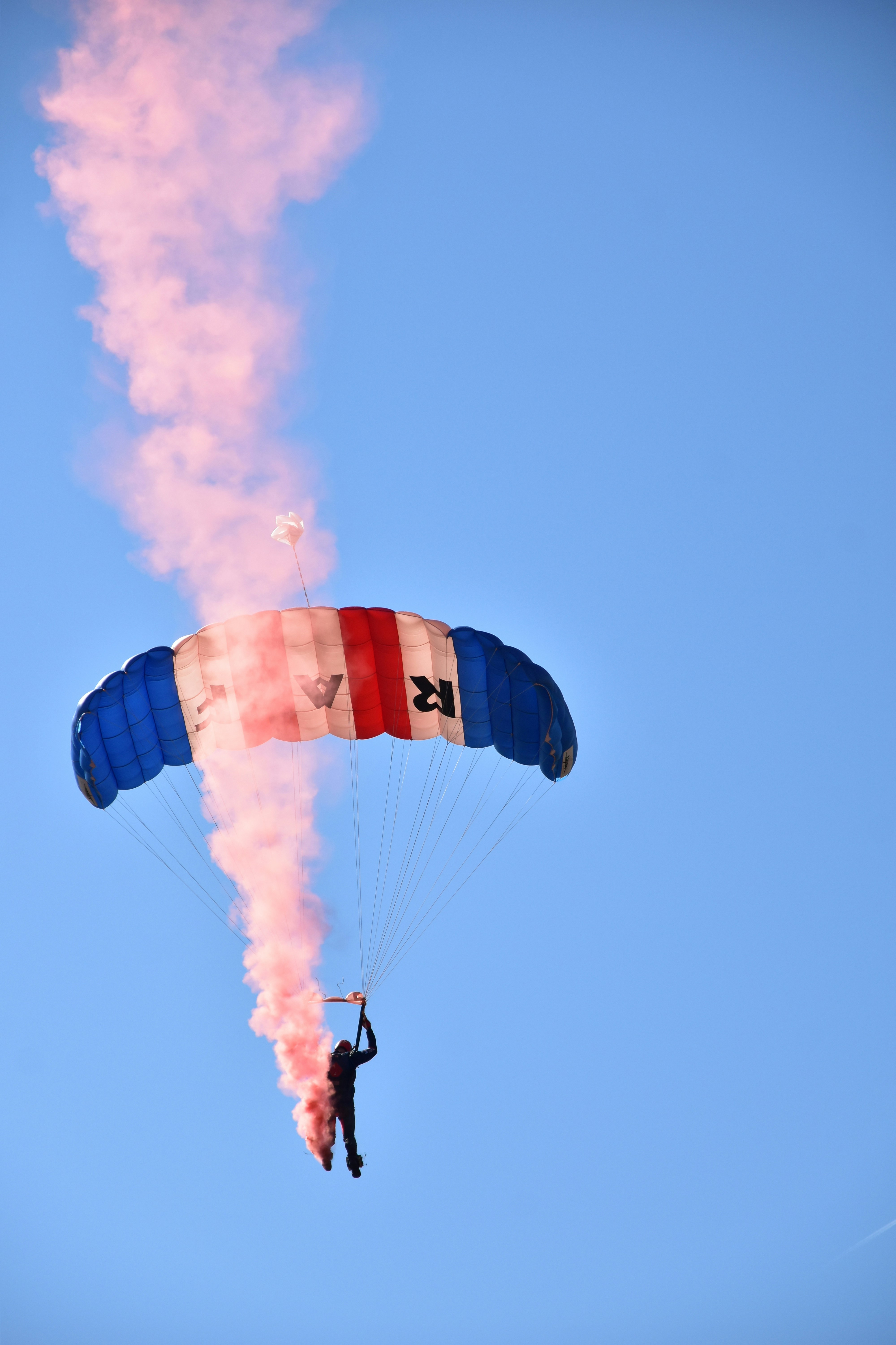 A skyward descent: parachutist trailing pink plume beneath a tri‑colored canopy