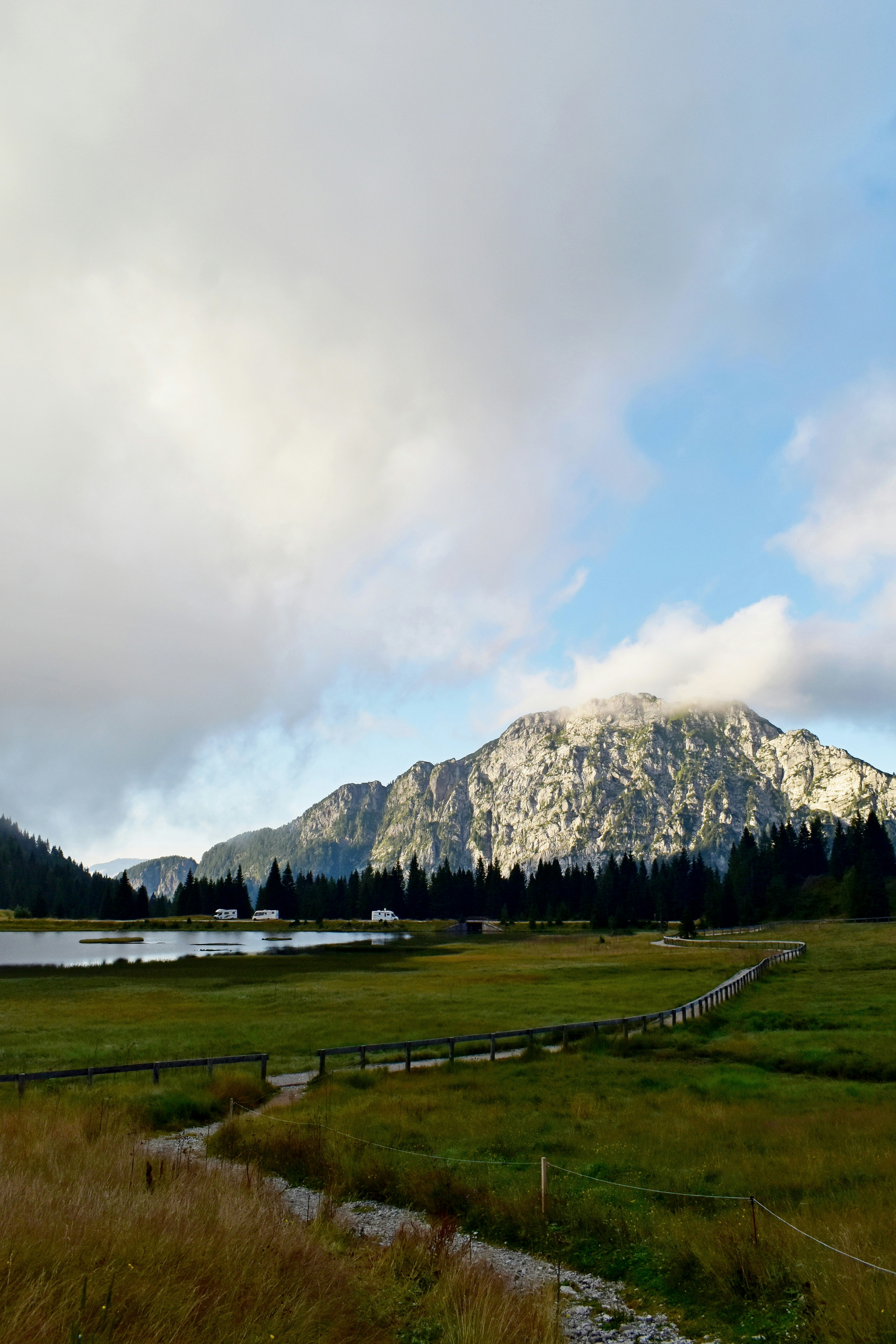 Threshold of calm: meadow, lake, and towering peak under a shifting sky