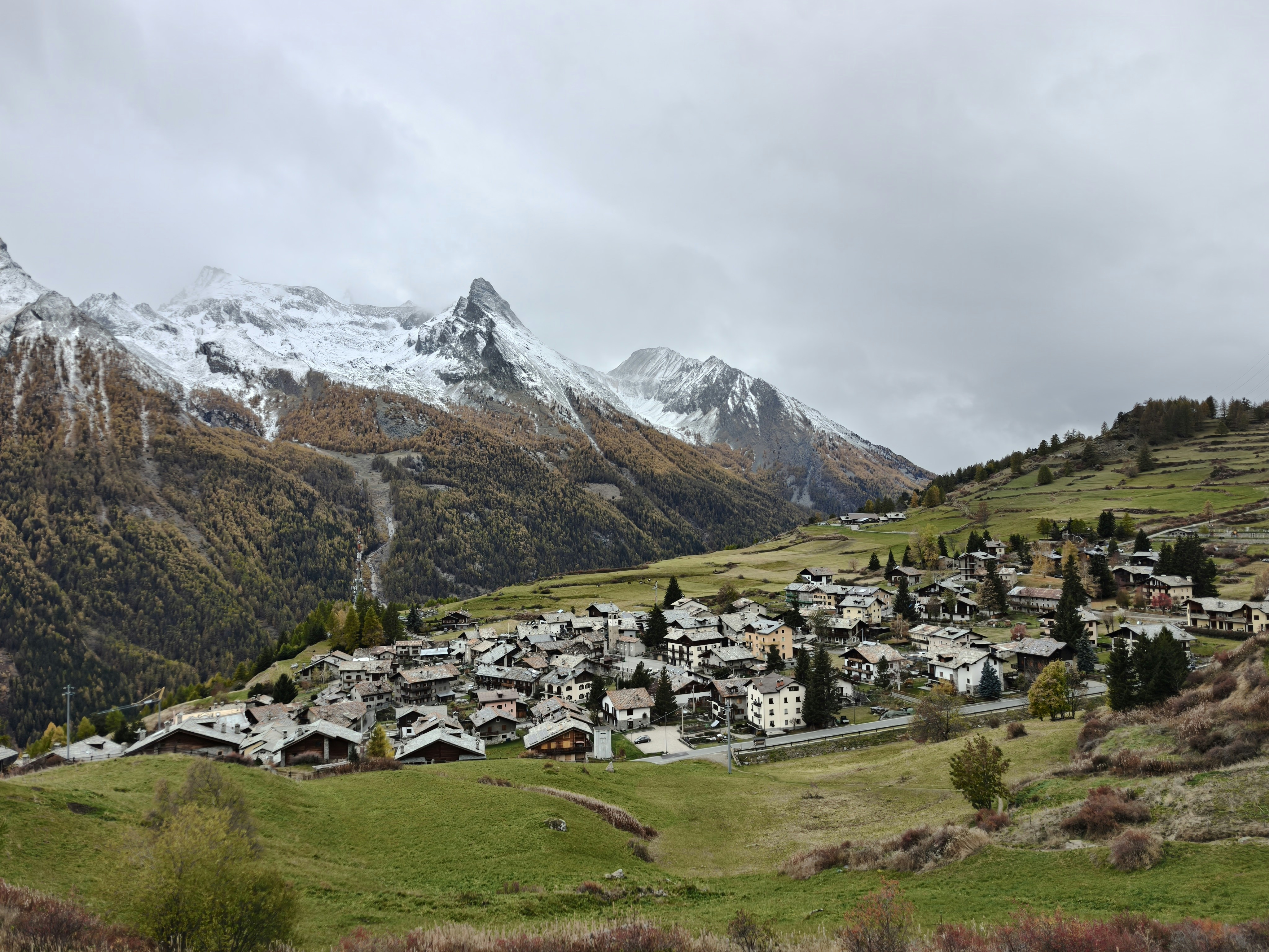 Gimillan Village Overlooking the Snowy Aosta Valley Alps Early autumn snow settles over the mountain peaks surrounding Gimillan, a small village above Cogne in the Aosta Valley. The yellow larch trees contrast with the white slopes, showing the first signs of winter in the Italian Alps.