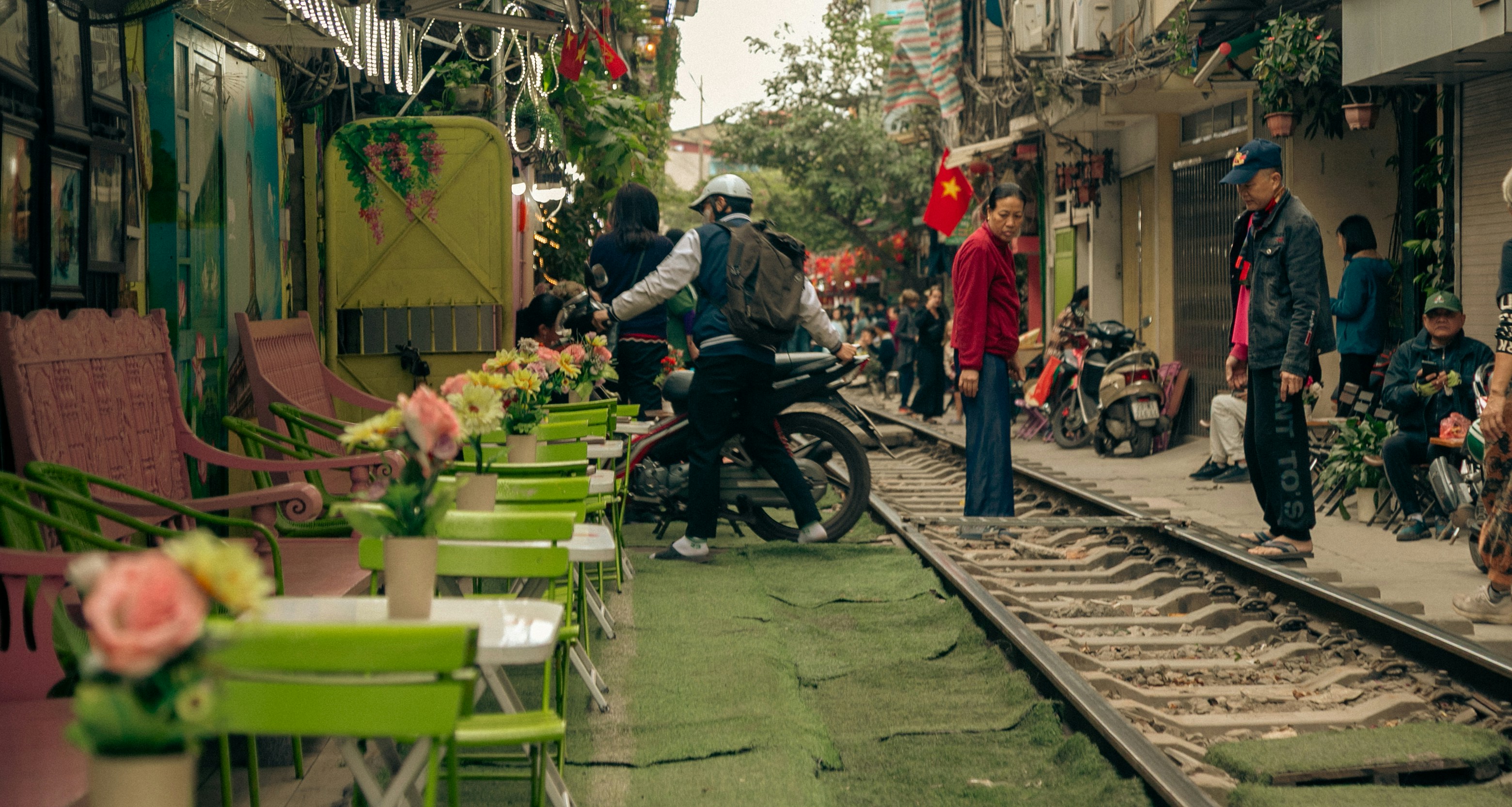 Railside Café in Motion: A Bustling Street Scene Along Narrow-Gauge Tracks