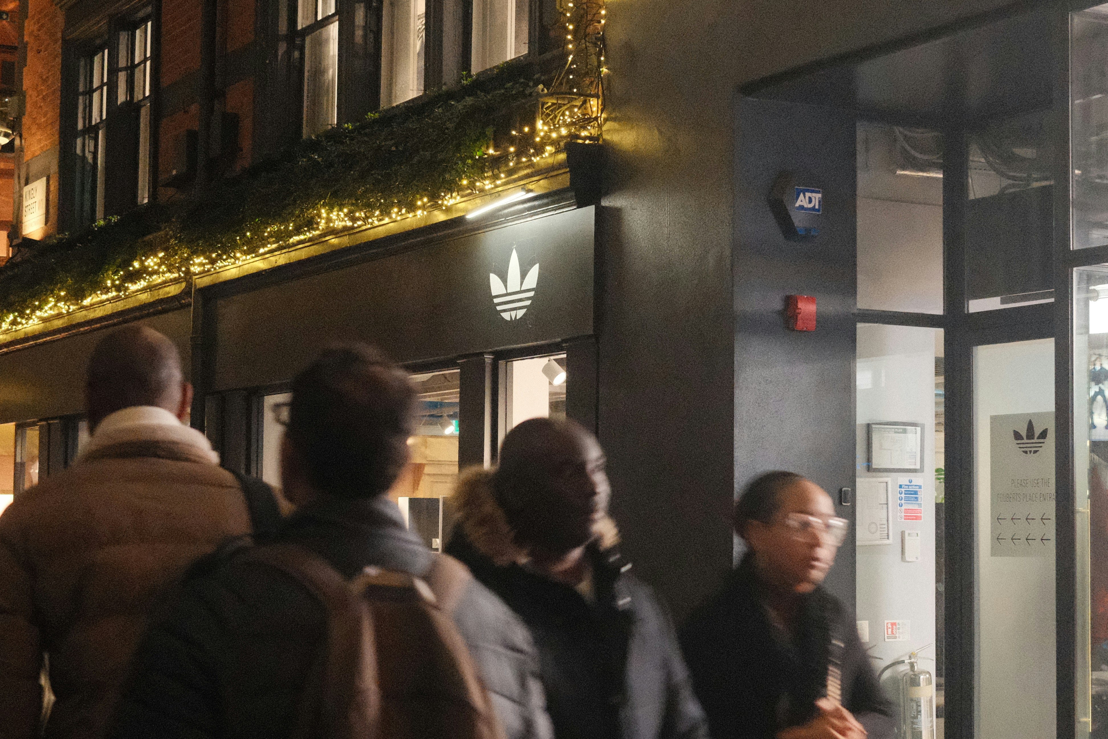 Urban anonymity beneath a glowing Adidas storefront