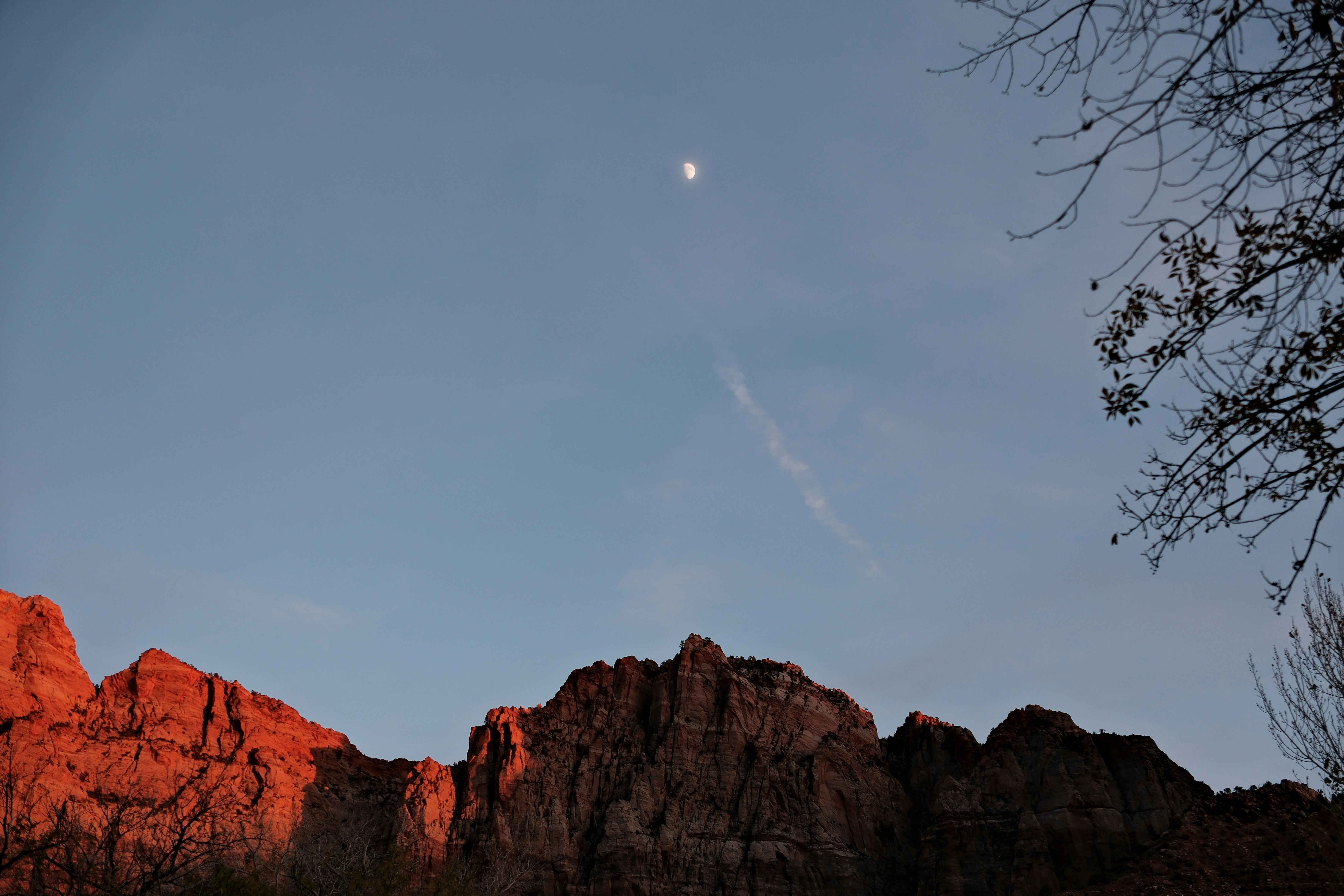 Dawn light on red cliff silhouettes under a crescent moon