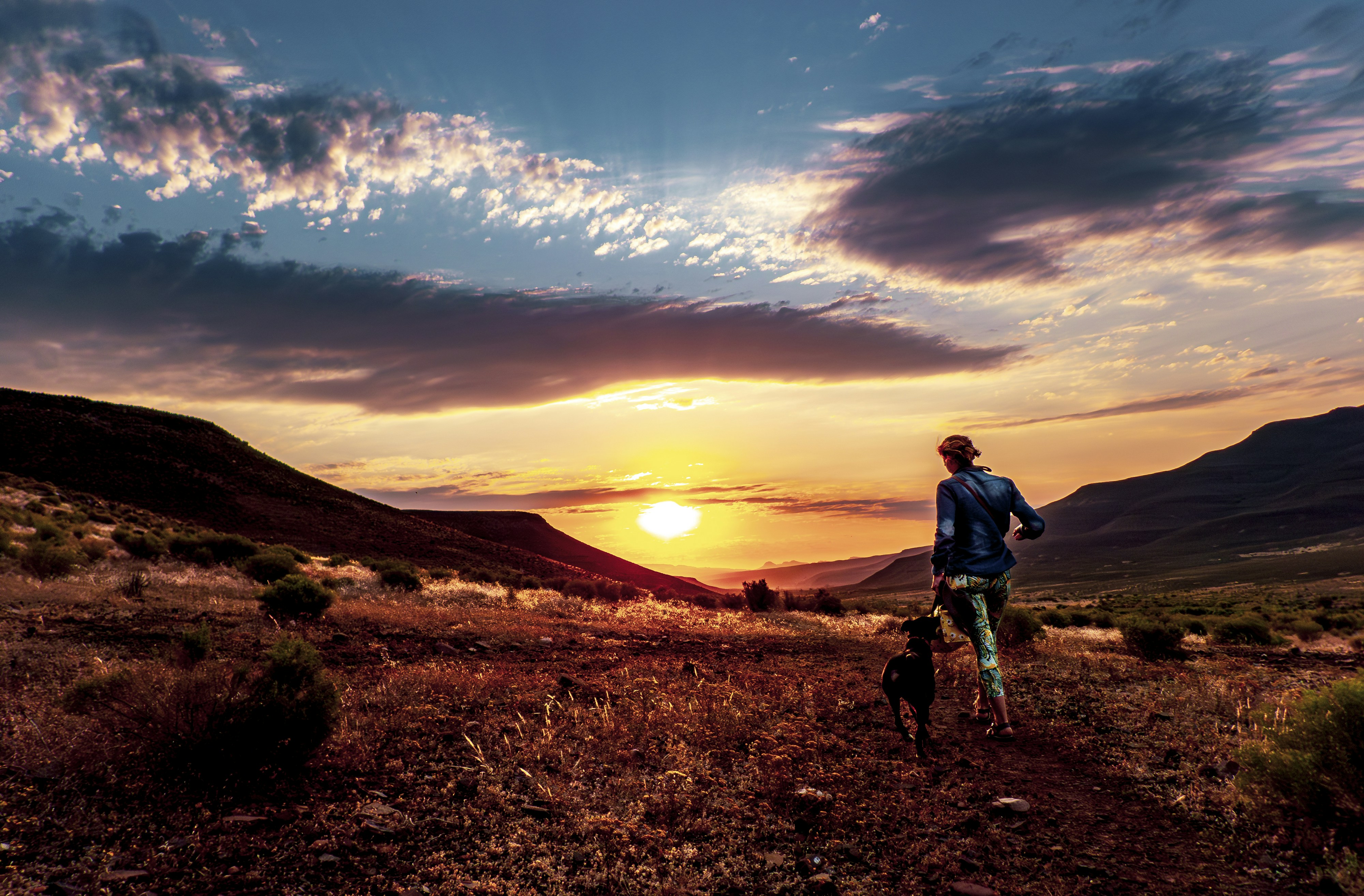 A woman takes her dog for a walk at sunset in the Cederberg. There is a raw empty beauty to this place.