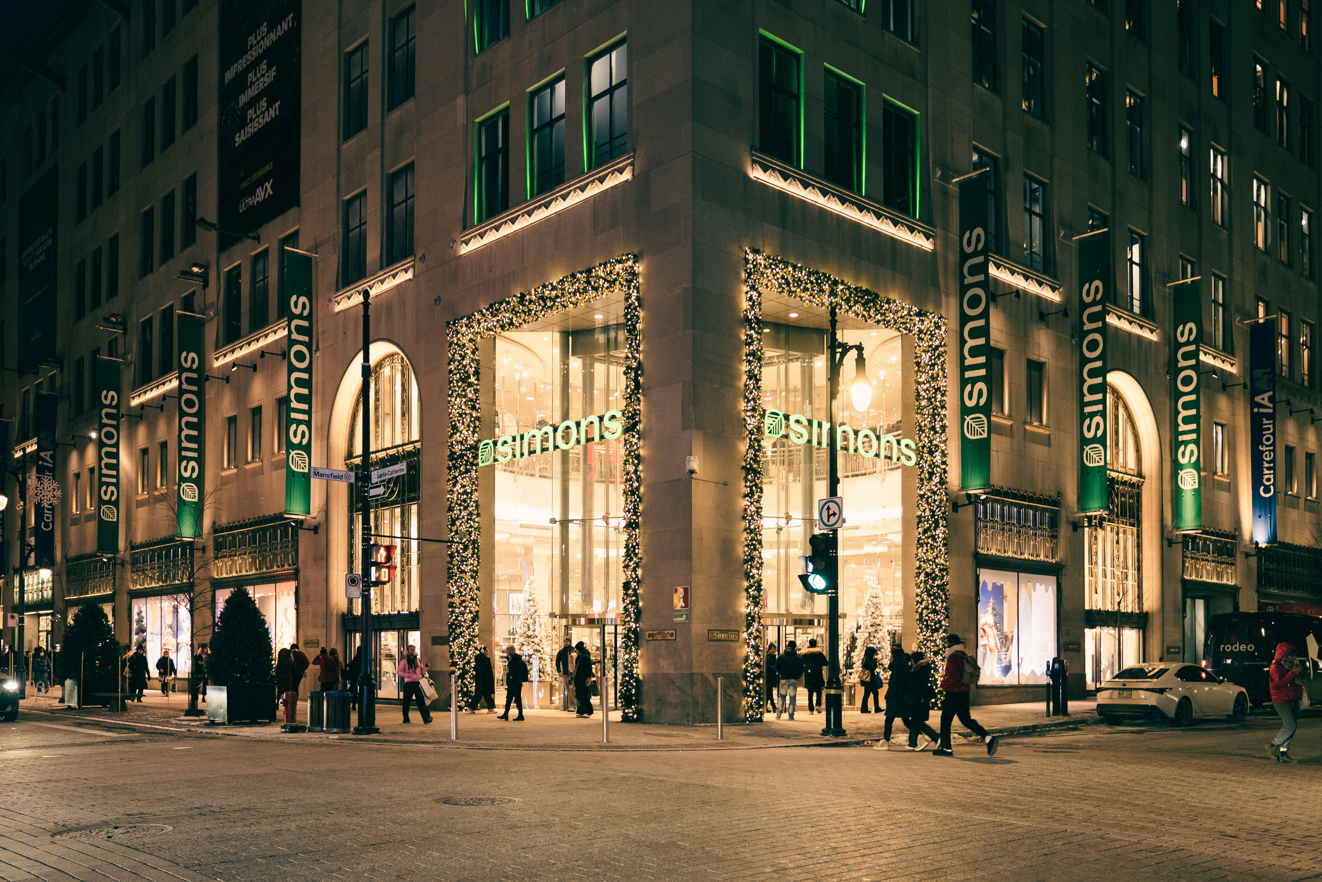 Corner department store illuminated at night with people.