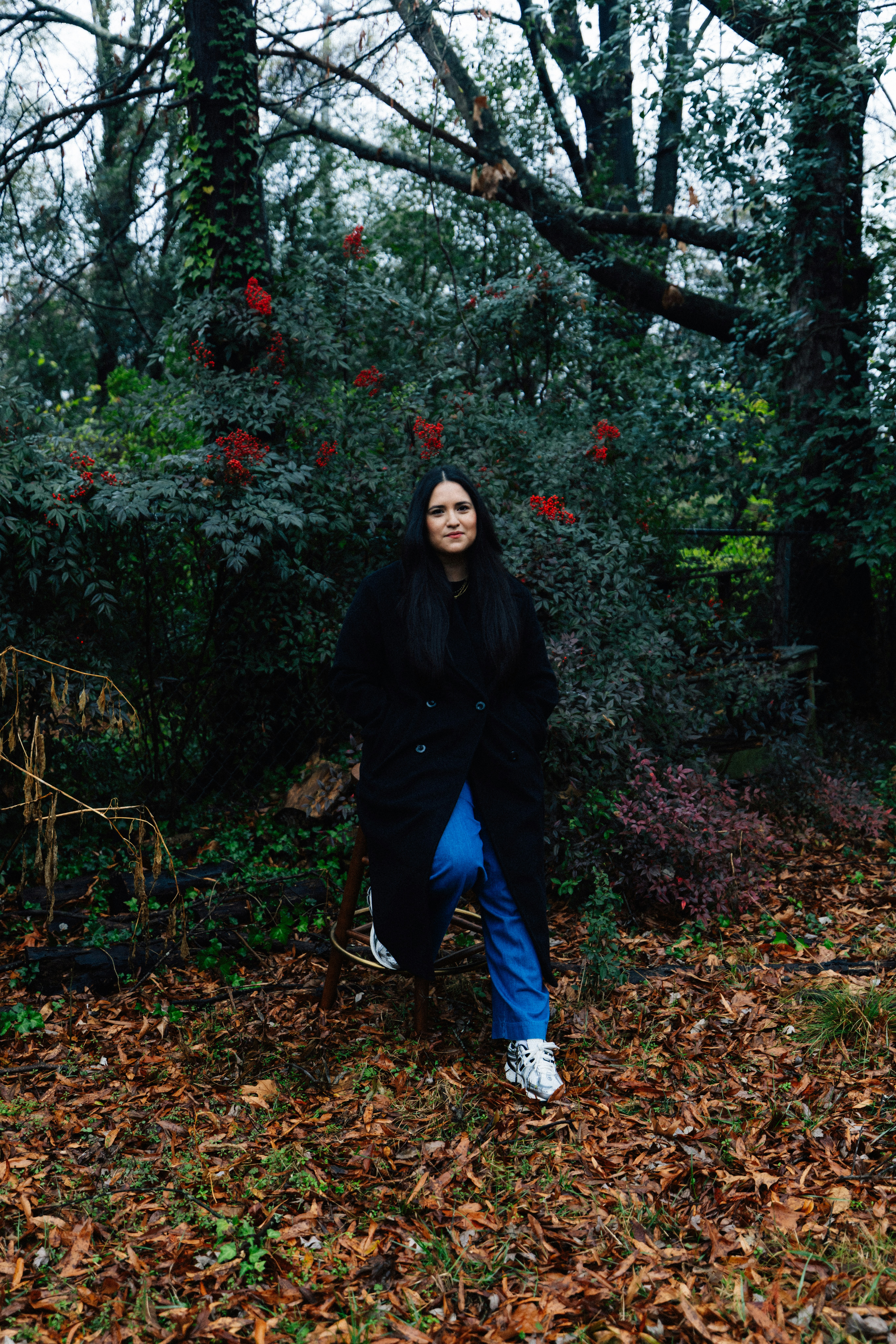 Woman in a black coat amid autumn foliage anchored by red berries