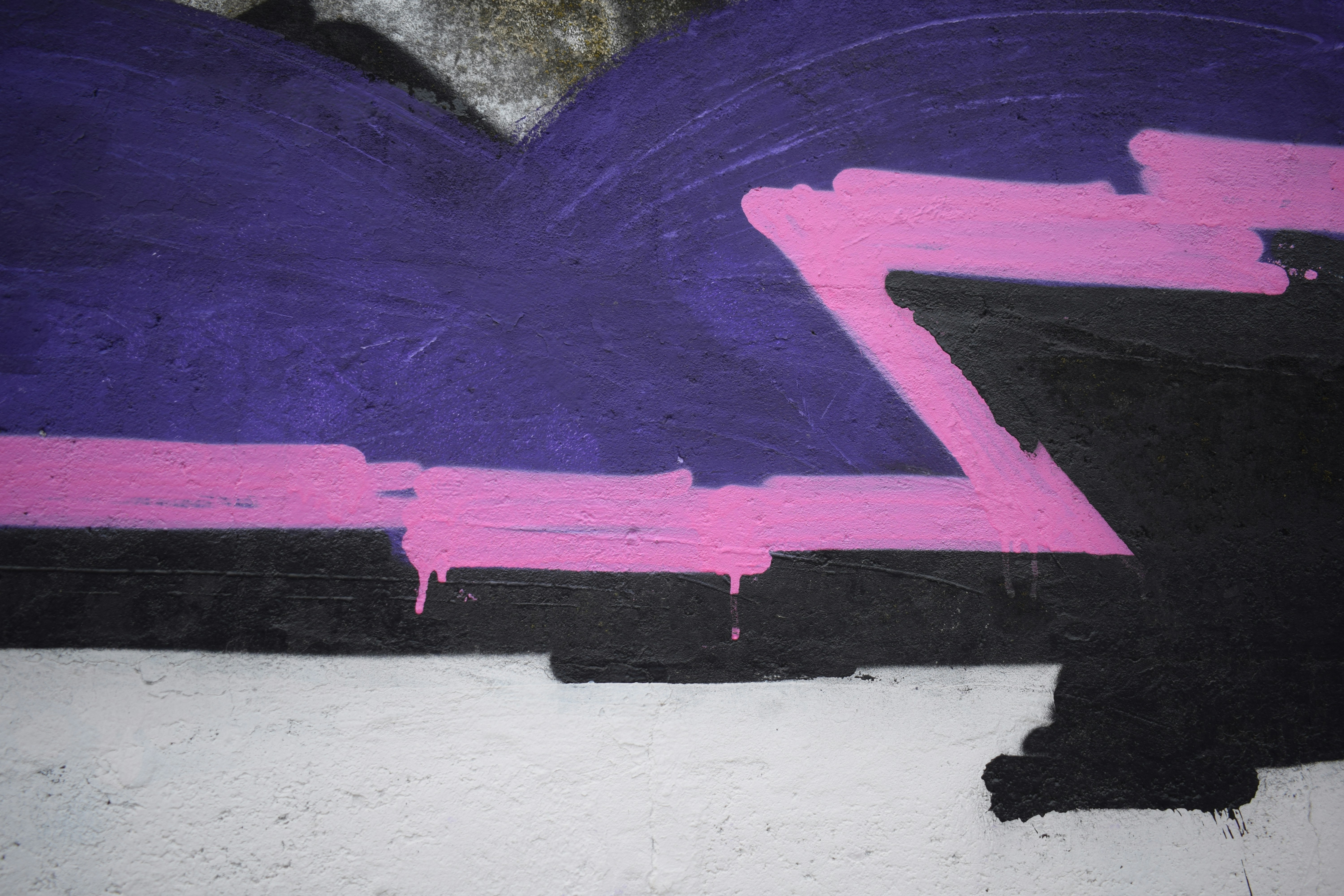 Purple graffiti arc and pink zigzag on a rough white wall