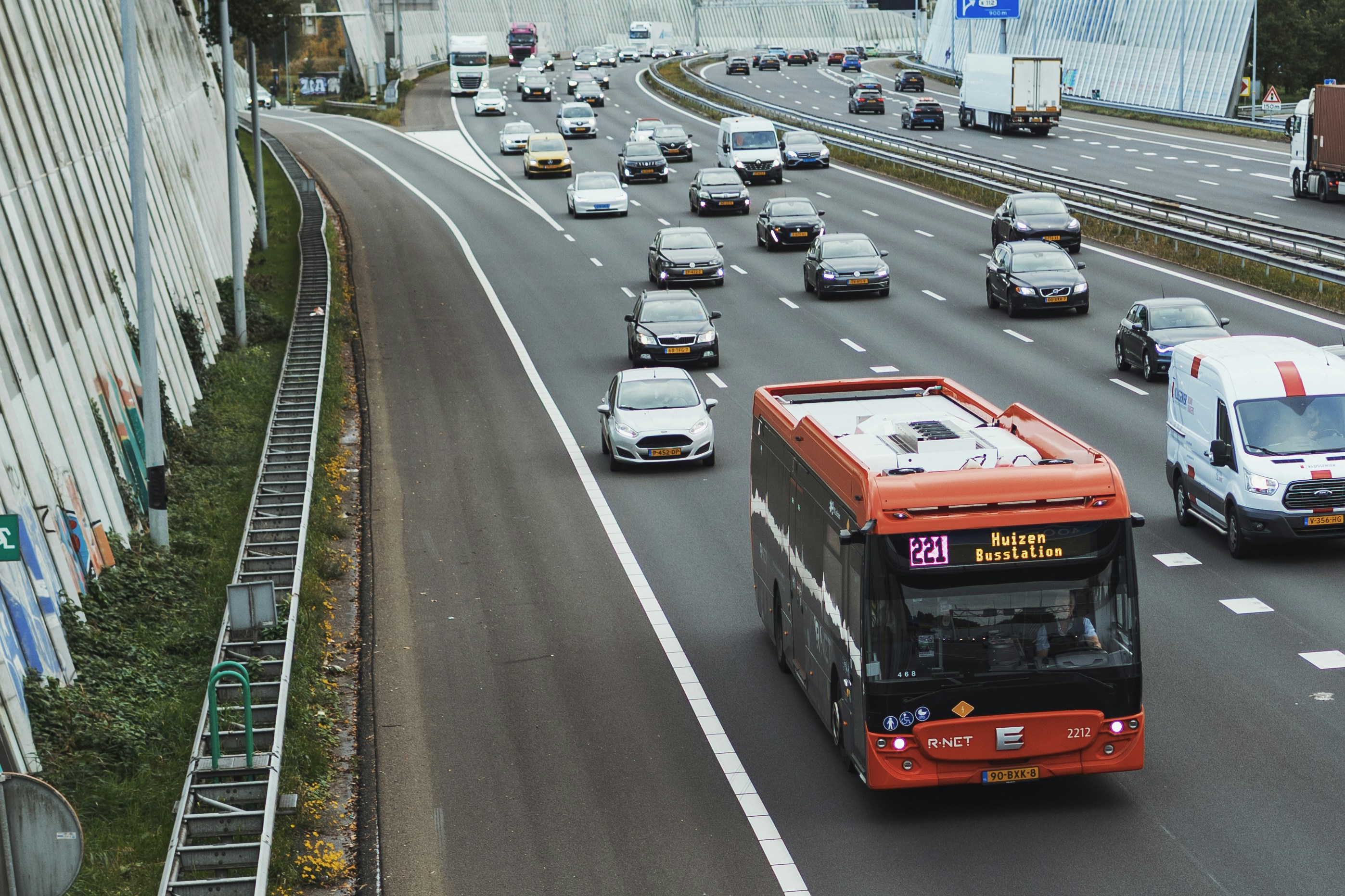 An R-NET bus heads to Huizen on the A10 ring road around Amsterdam, weaving through traffic on an overcast autumn day in the Netherlands.