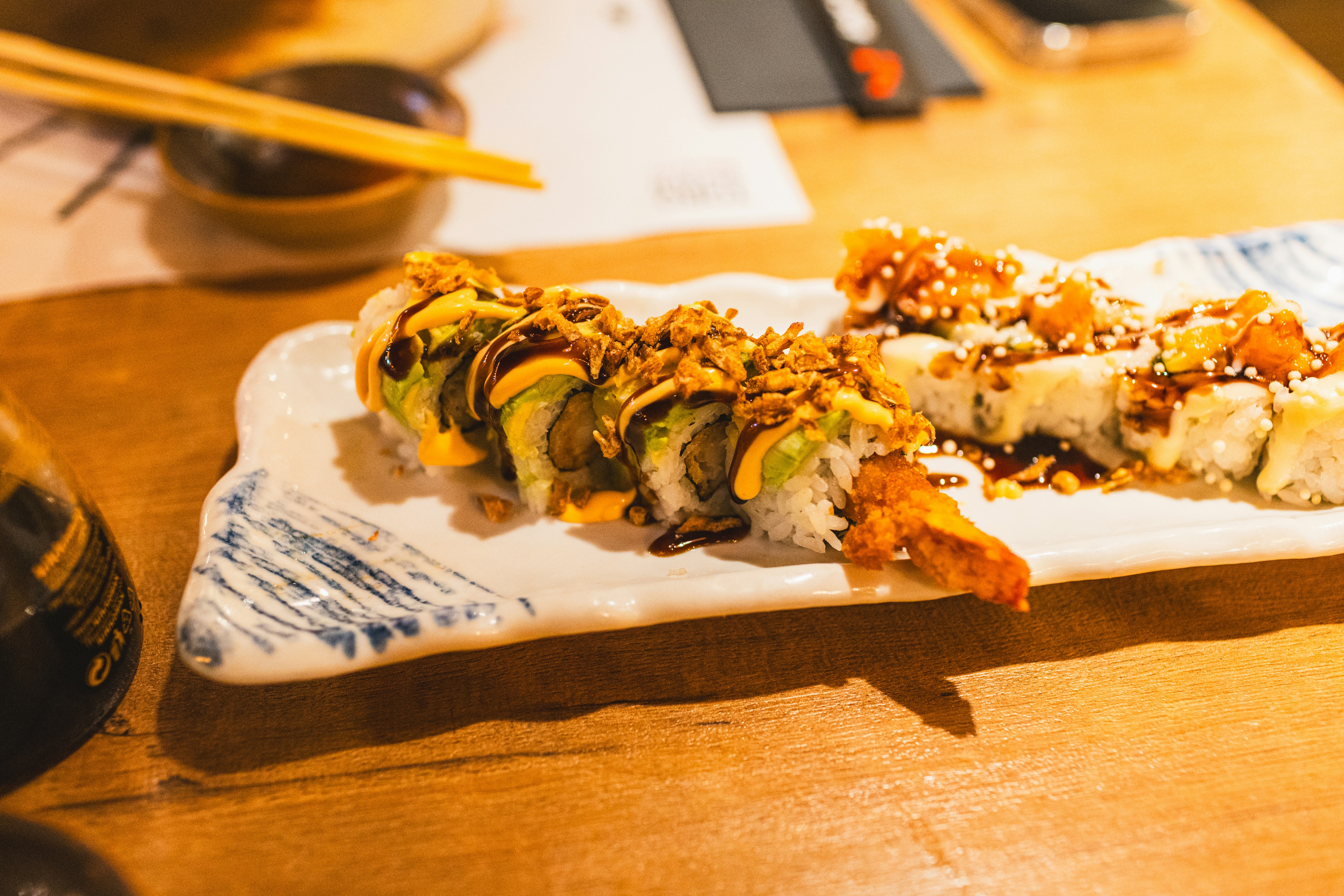 Sushi lineup on a ceramic plate: crisp rolls with sesame drizzle and crunch at a casual dine-in.