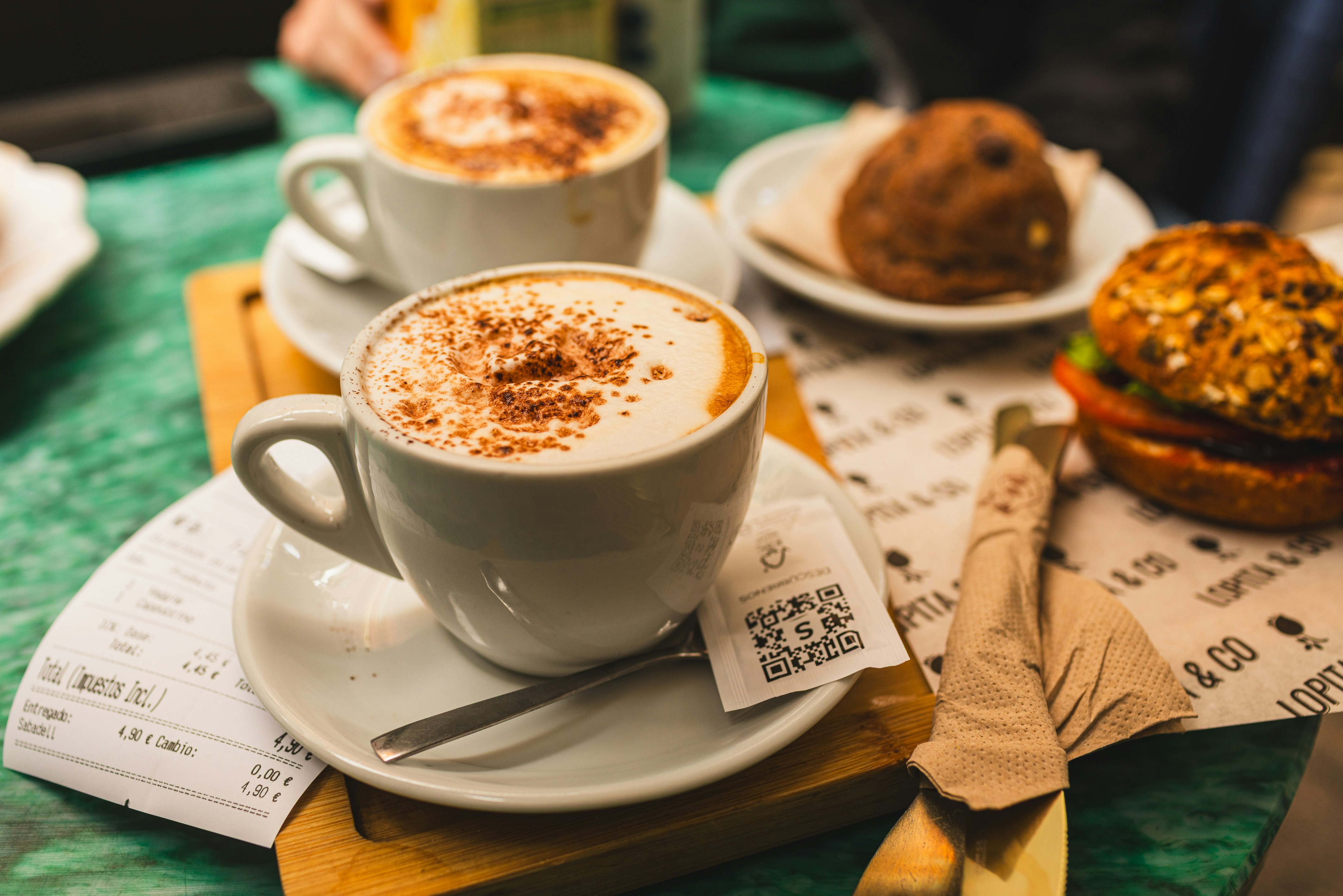 Creamy cappuccino on a wooden board, with a sesame bun and a baked pastry in a cozy café
