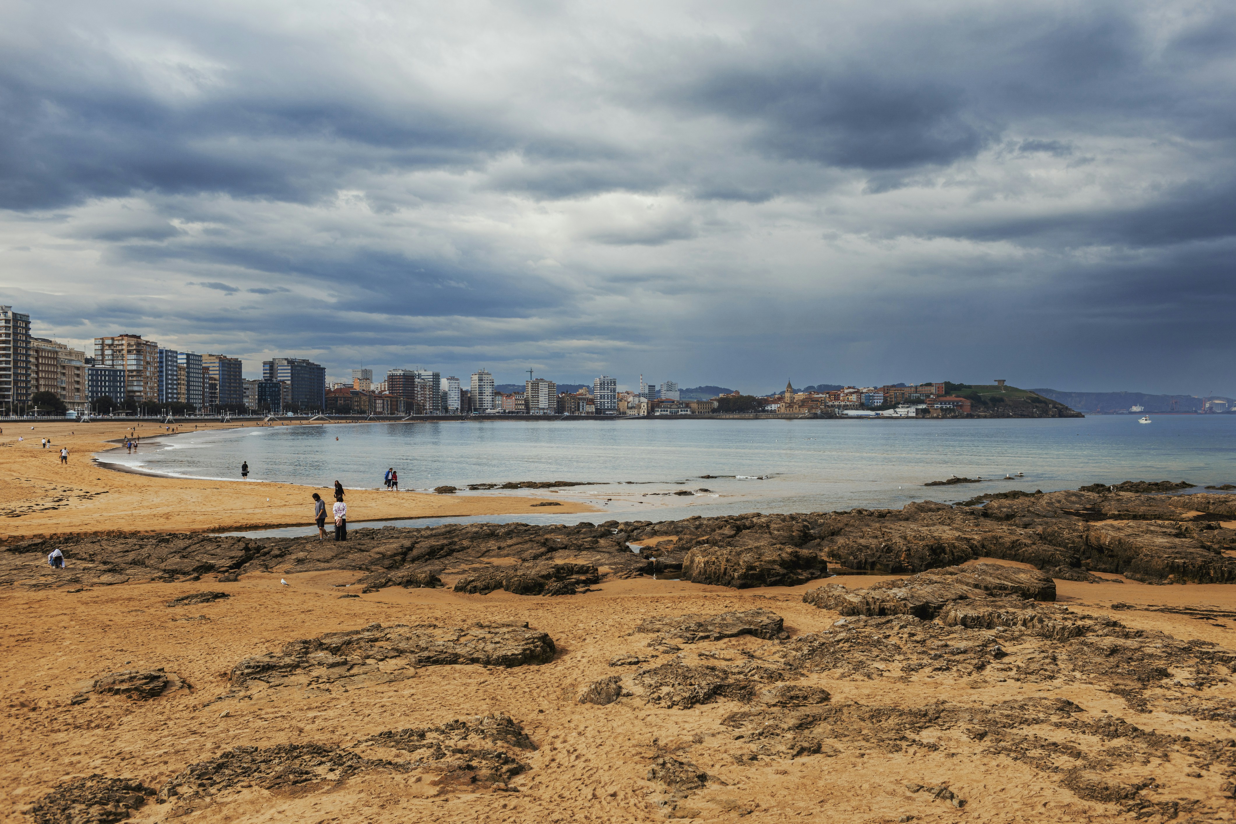 Curved shoreline and distant cityscape under dramatic coastal skies