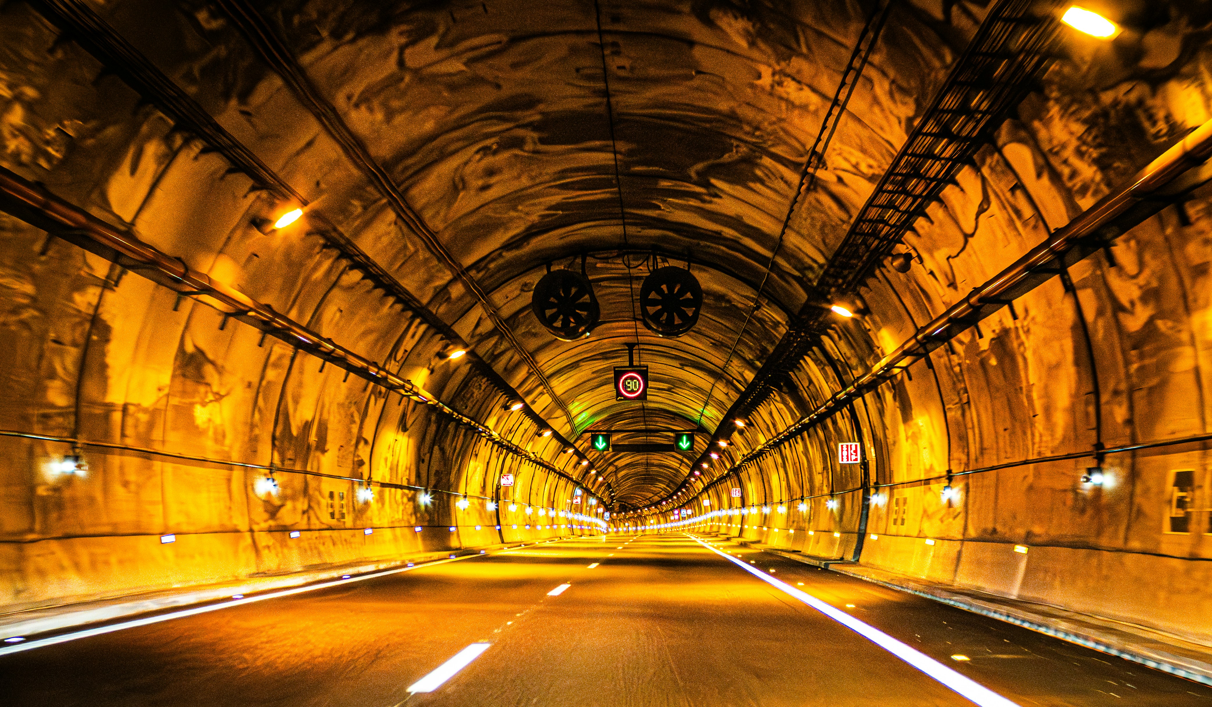 A golden-lit highway tunnel stretches ahead on the road from Oviedo to Bufones de Pria, its curved walls reflecting warm amber light as the road cuts through the Asturian mountains.