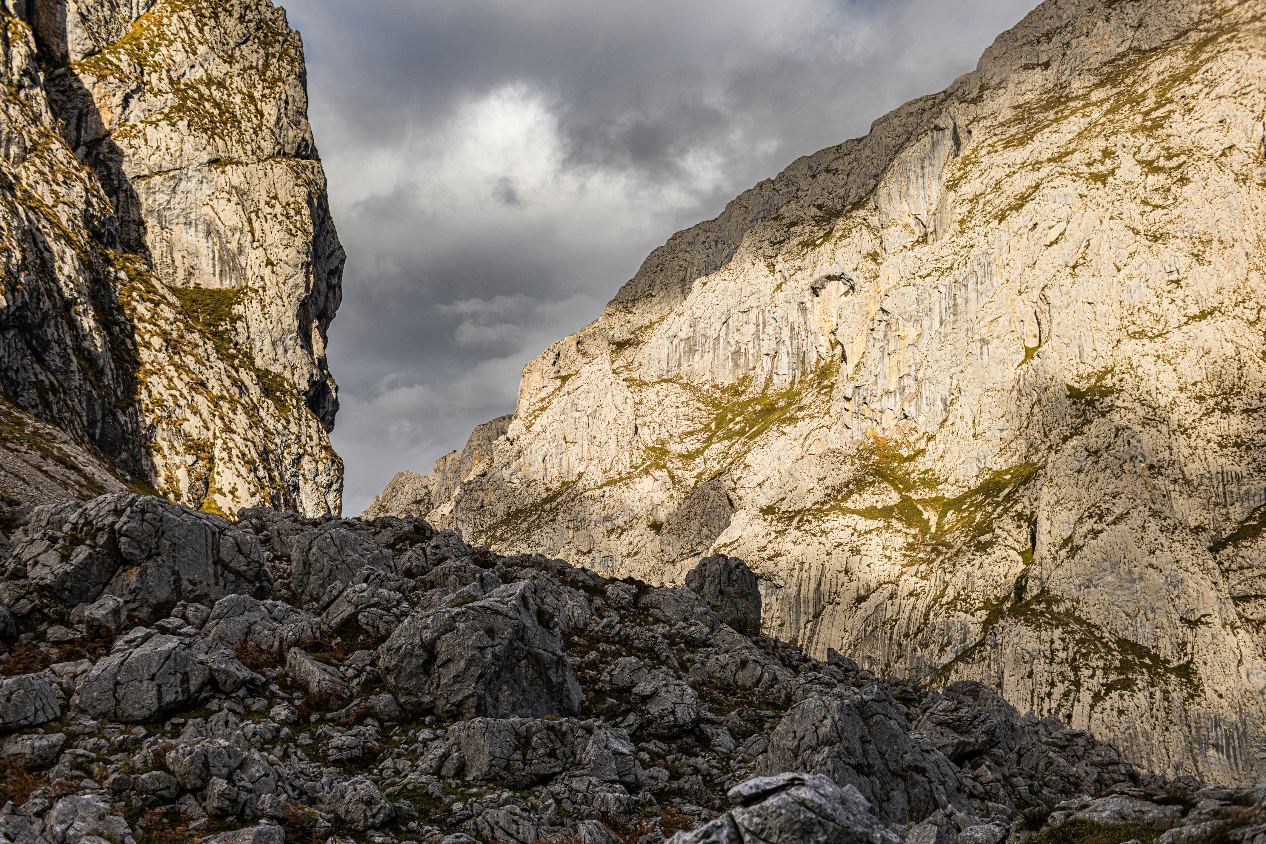 Sheer limestone cliffs catch golden light under stormy skies in Picos de Europa, rocky scree slopes tumbling into shadow near Bulnes.
