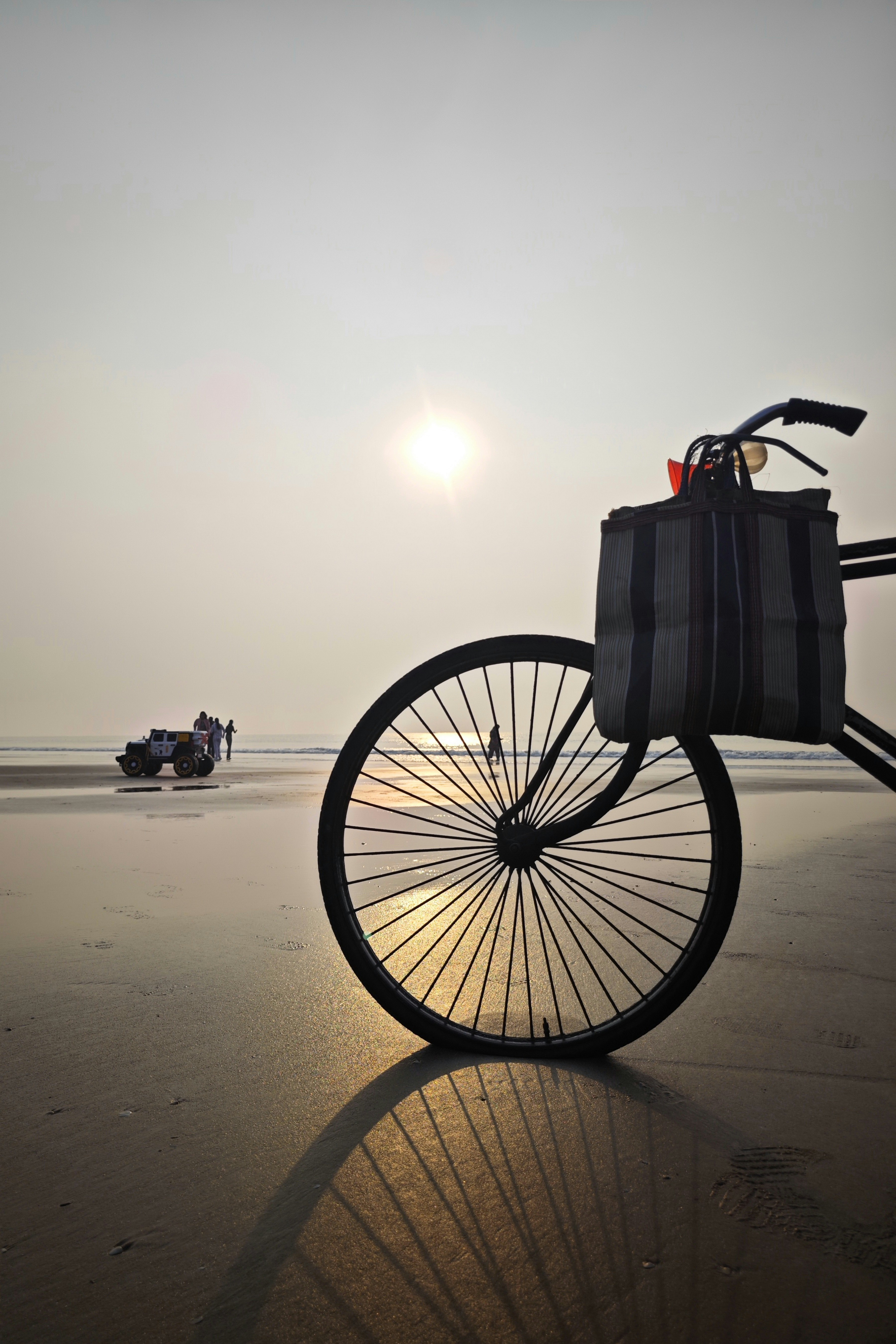 Bicycle on a beach at sunset with people in background.