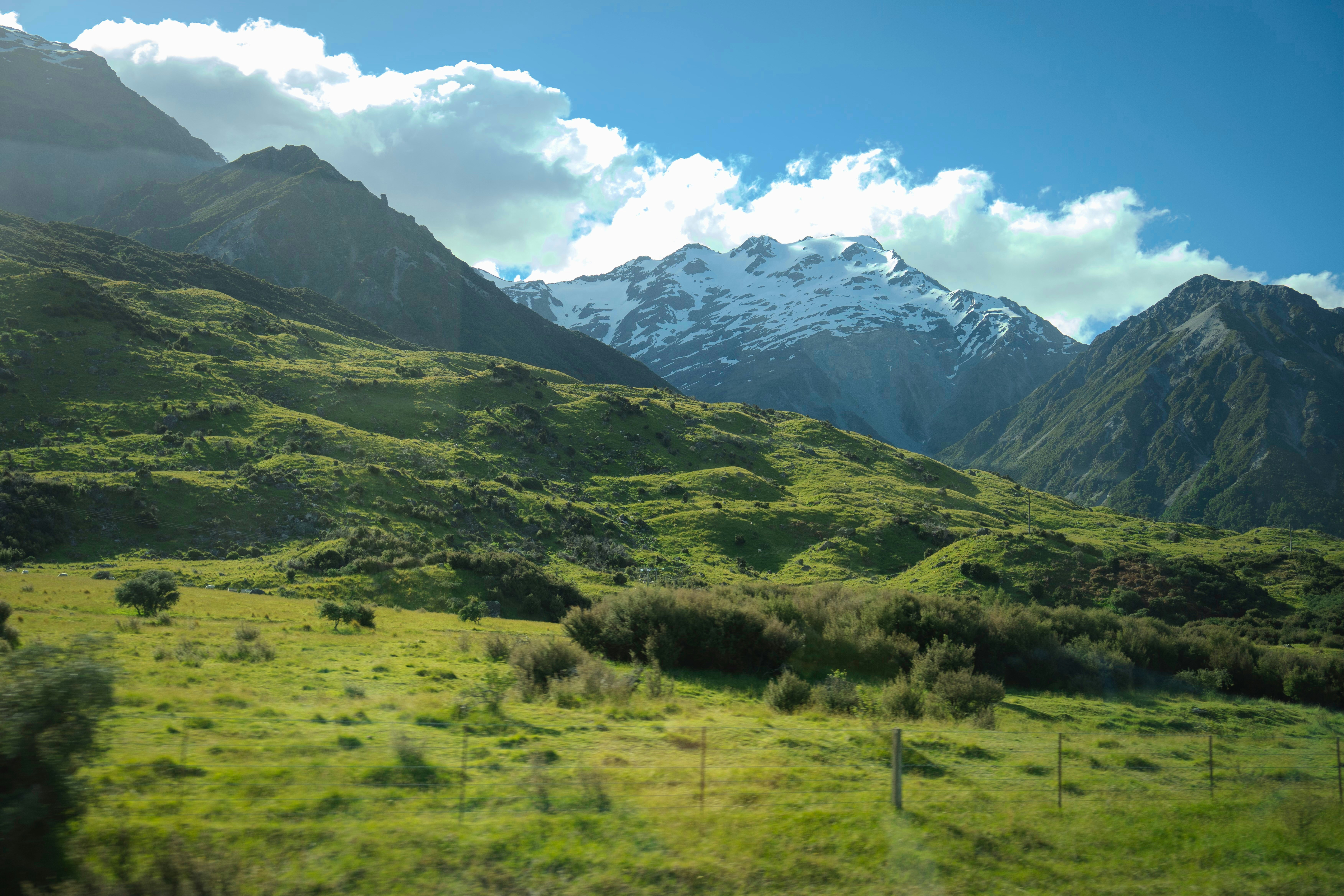 Green rolling hills with snow-capped mountains under a blue sky photo ...