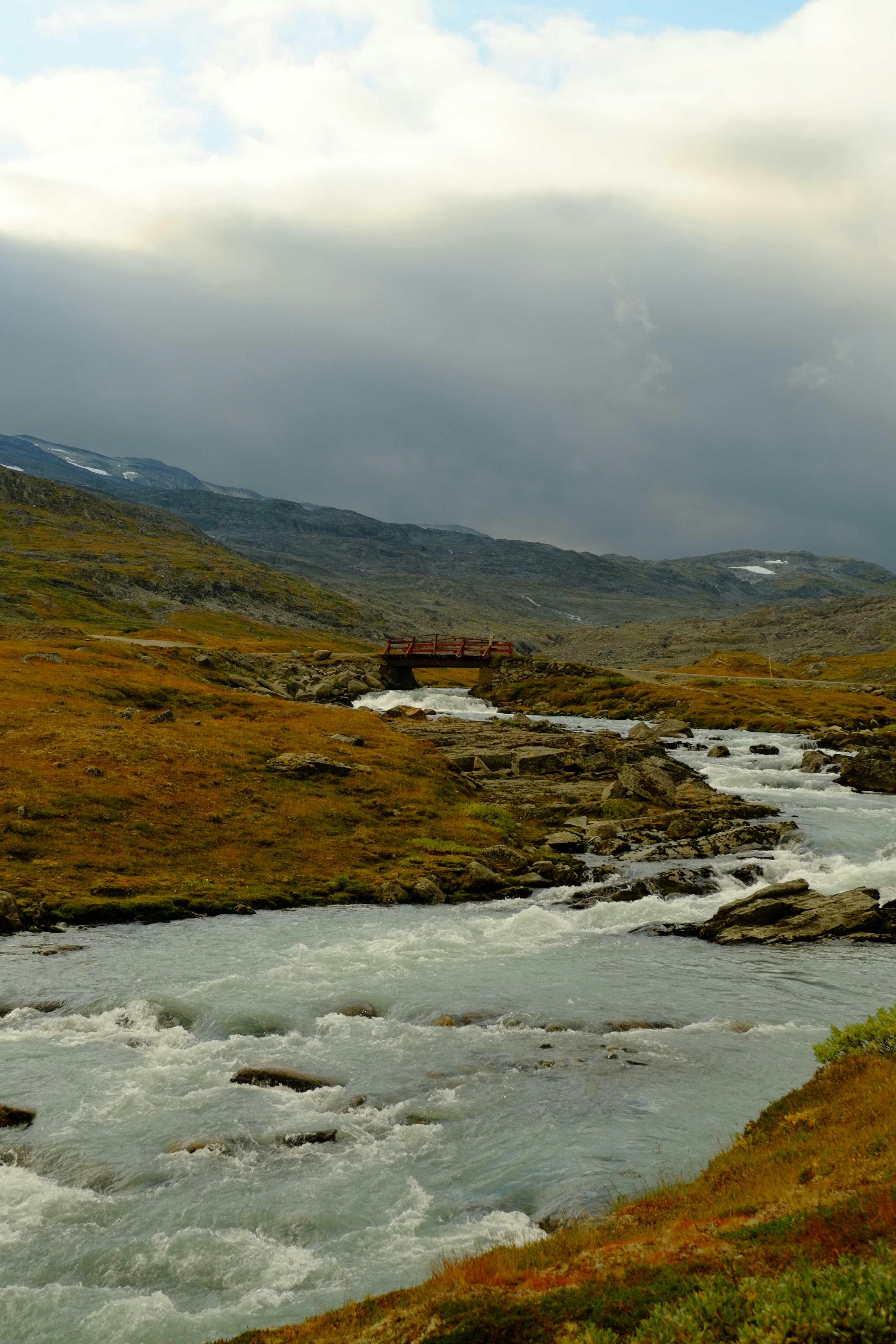 A Red Bridge Over a Mountain River Under Broad Skies