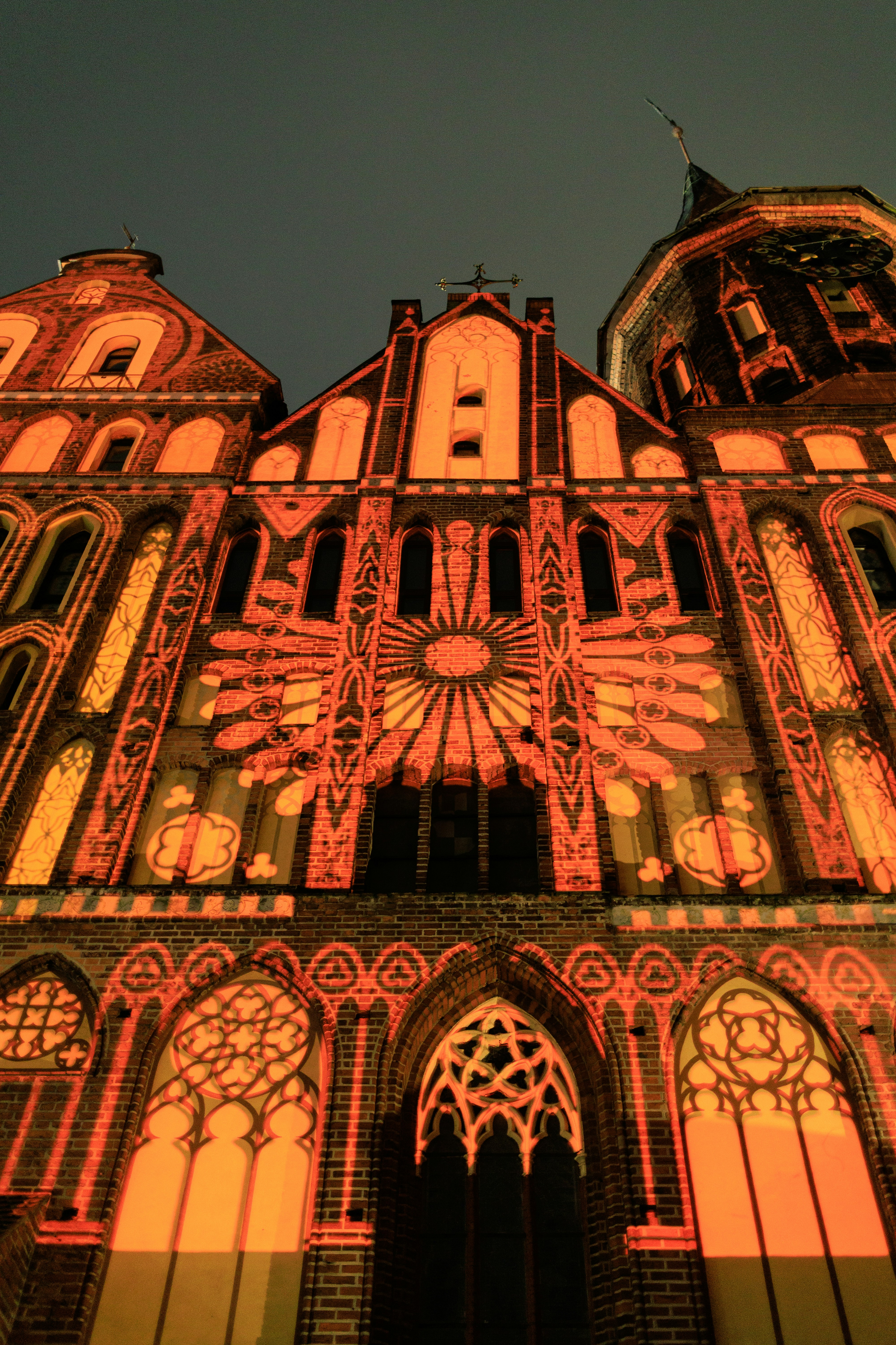 The Königsberg Cathedral on Kant Island in Kaliningrad is illuminated with intricate orange-and-yellow projected light patterns at night — a light show during the city festival.