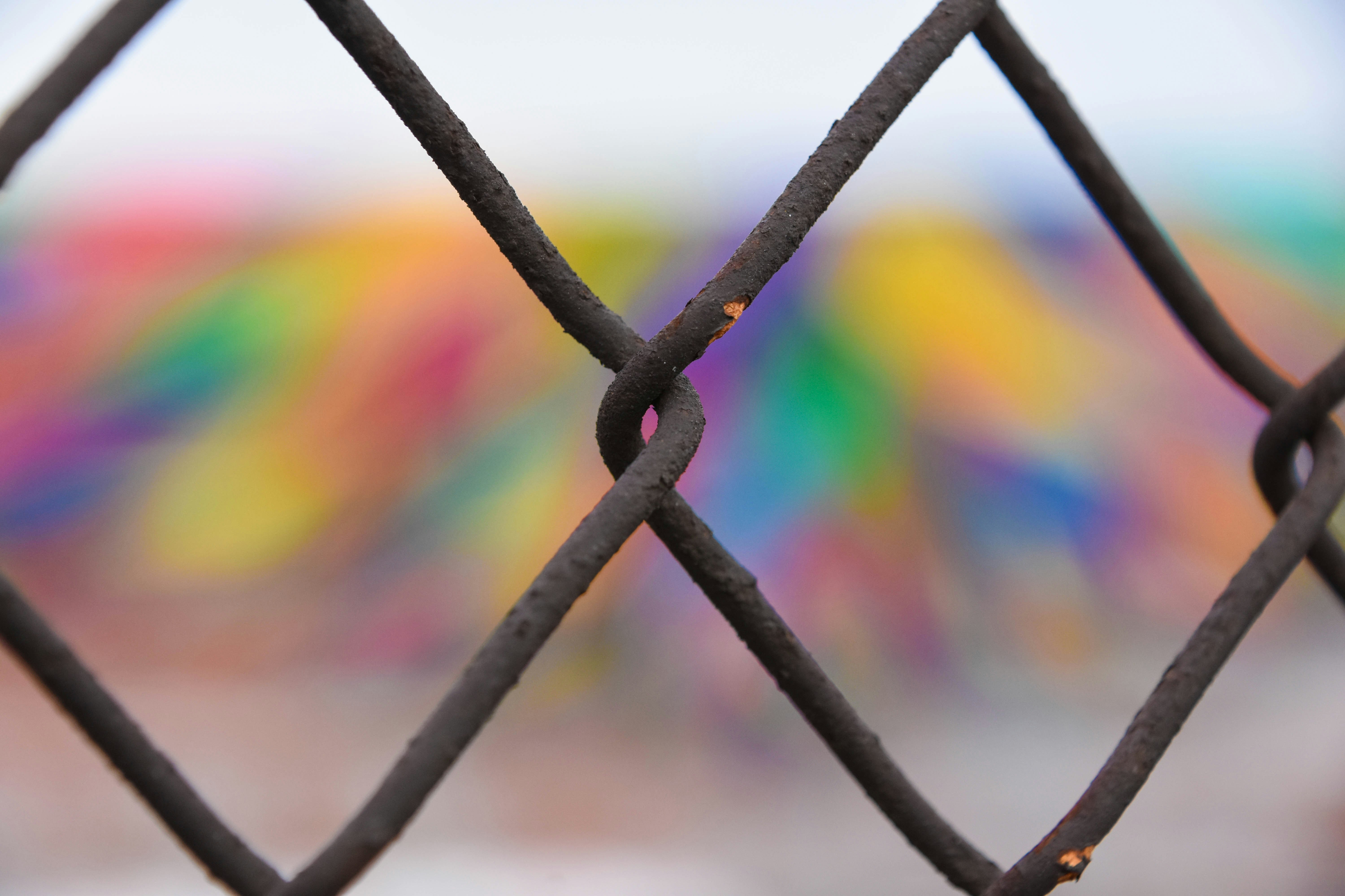 Between the Rails: Faded Color Burst Behind a Rusted Fence