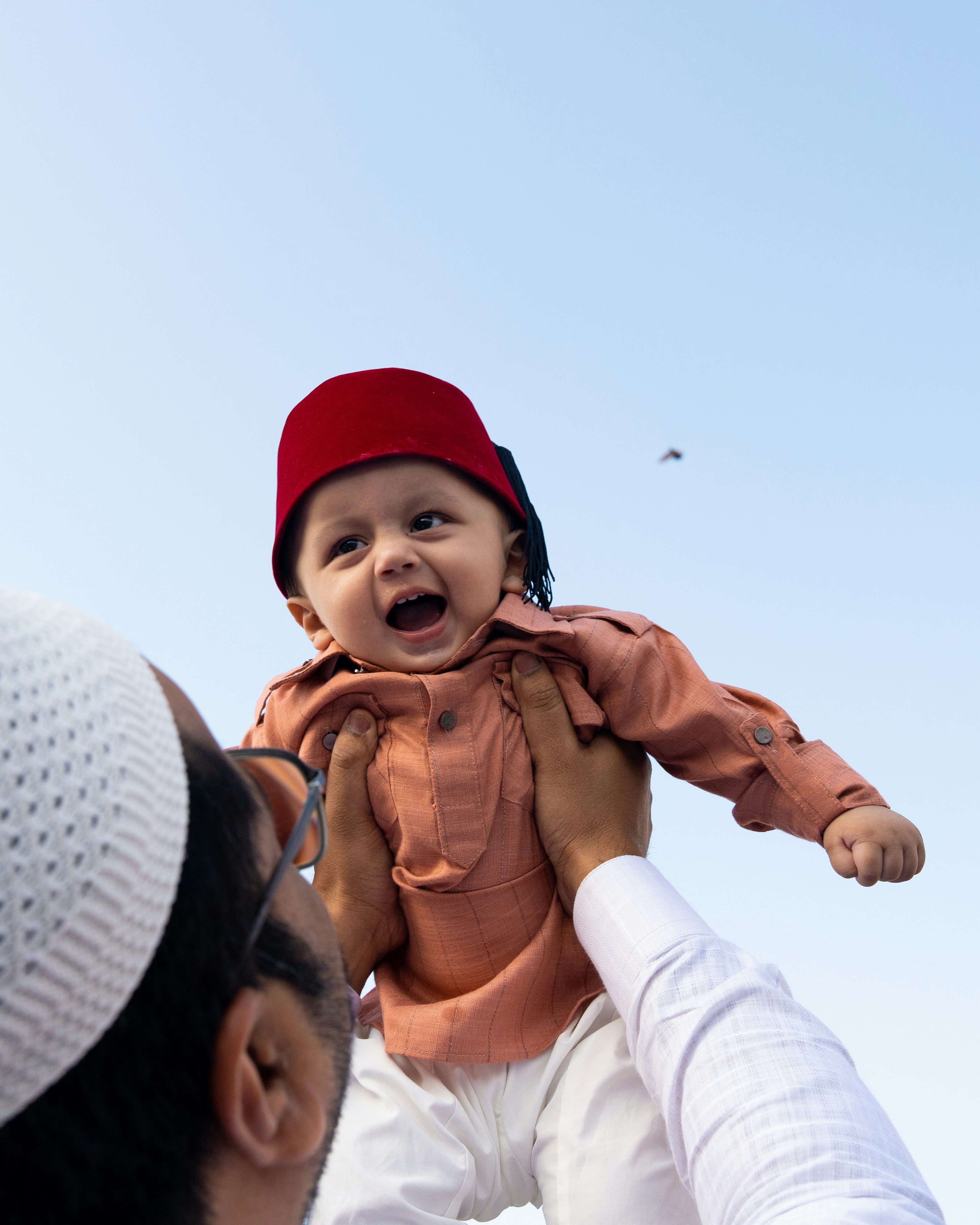 Joyful Lift: Baby in Red Cap Flung Toward the Sky