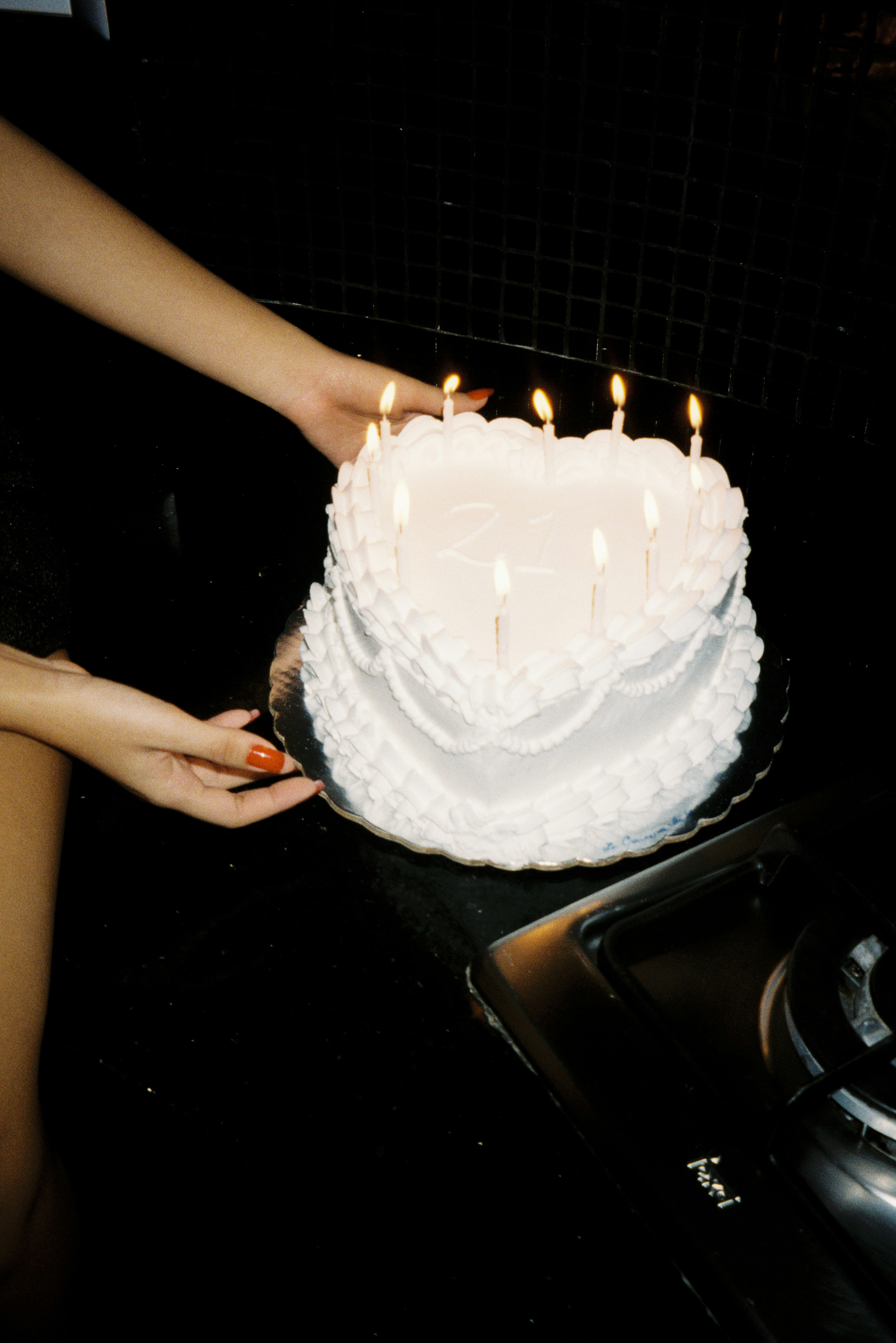 Candlelit Celebration: Hands Framing a White Frosted Cake