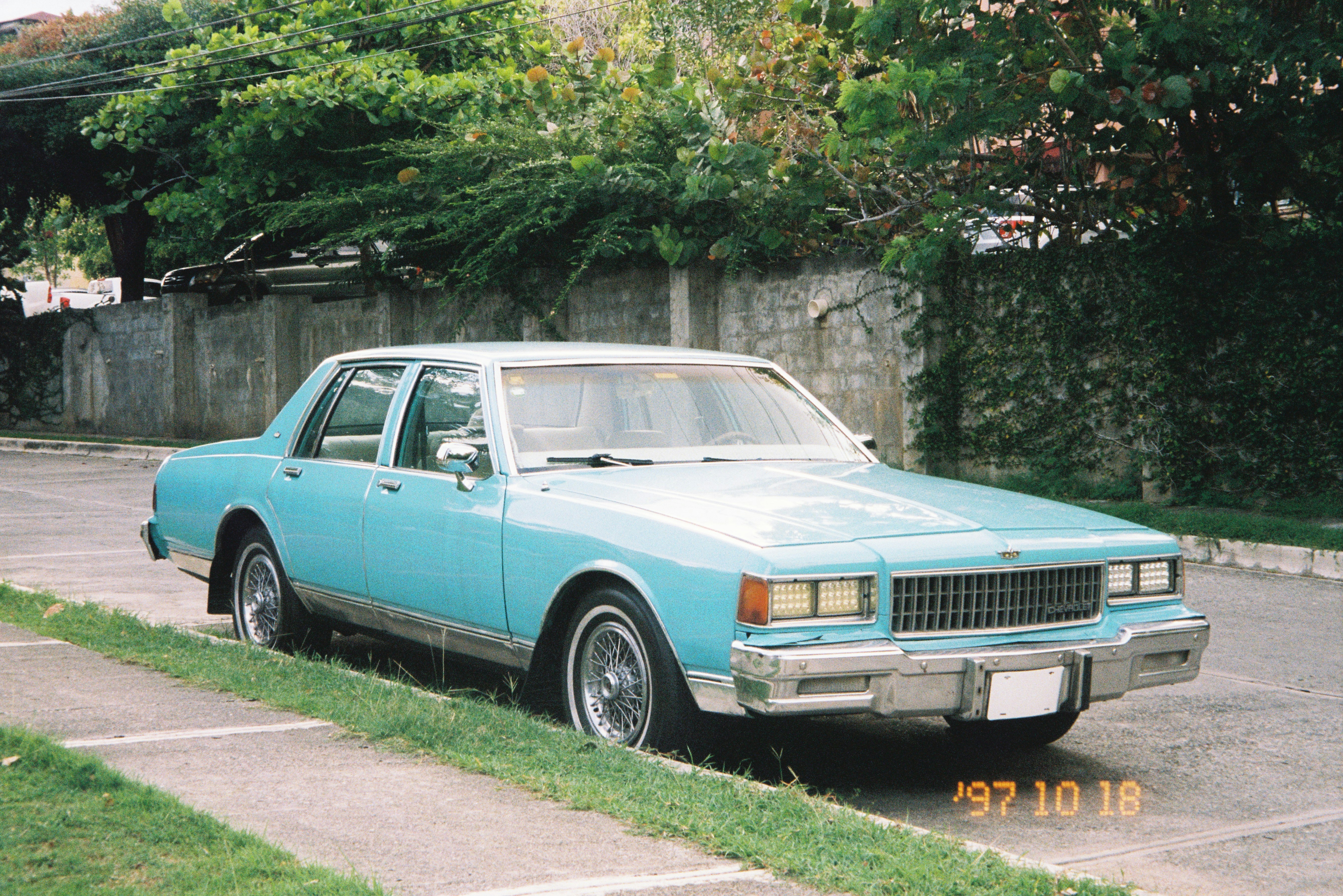 Turquoise Classic: A 1980s Sedan Rests by a Quiet Sidewalk