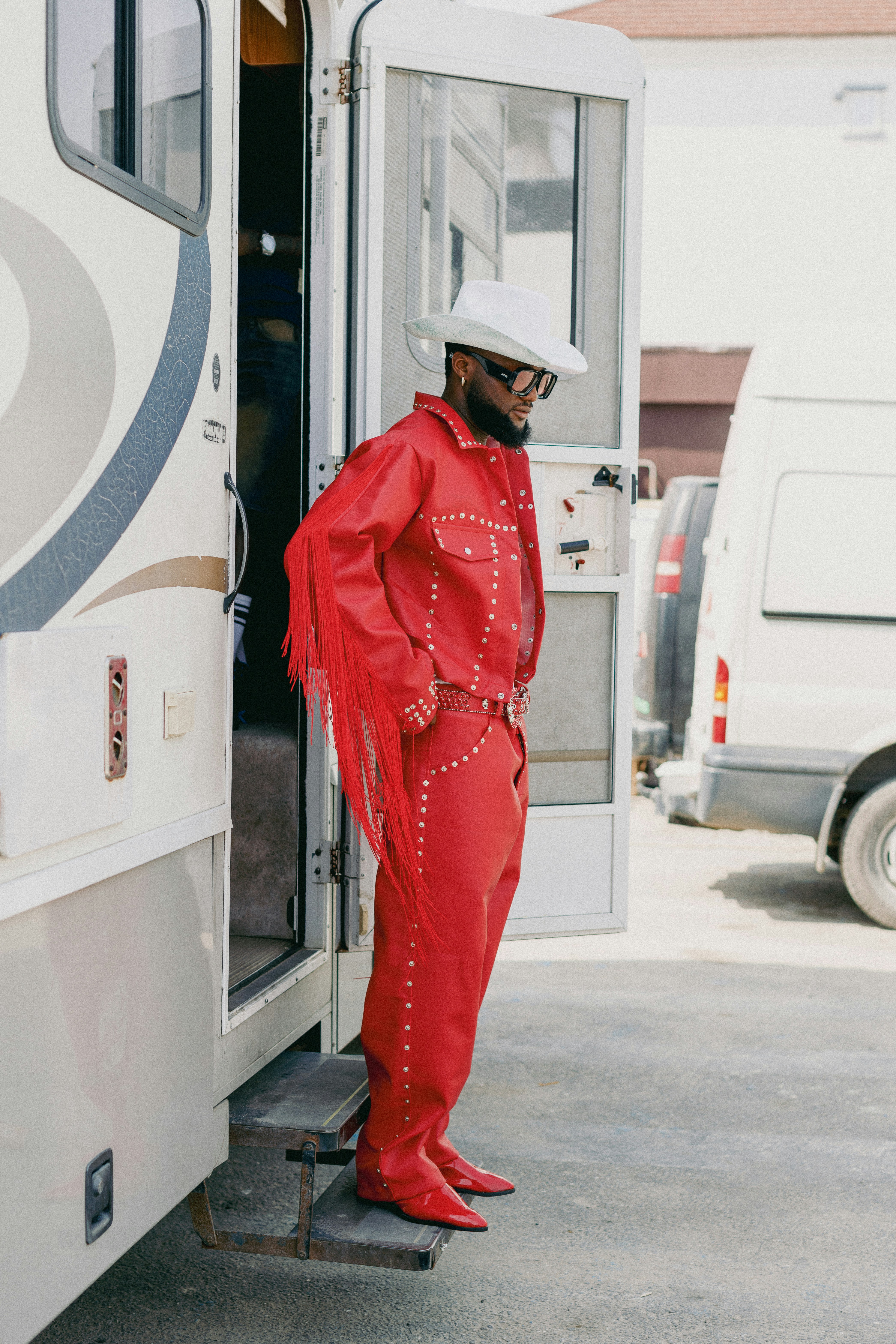 Red Fringed Ensemble Steps Off a Bus in a Deserted Parking Lot