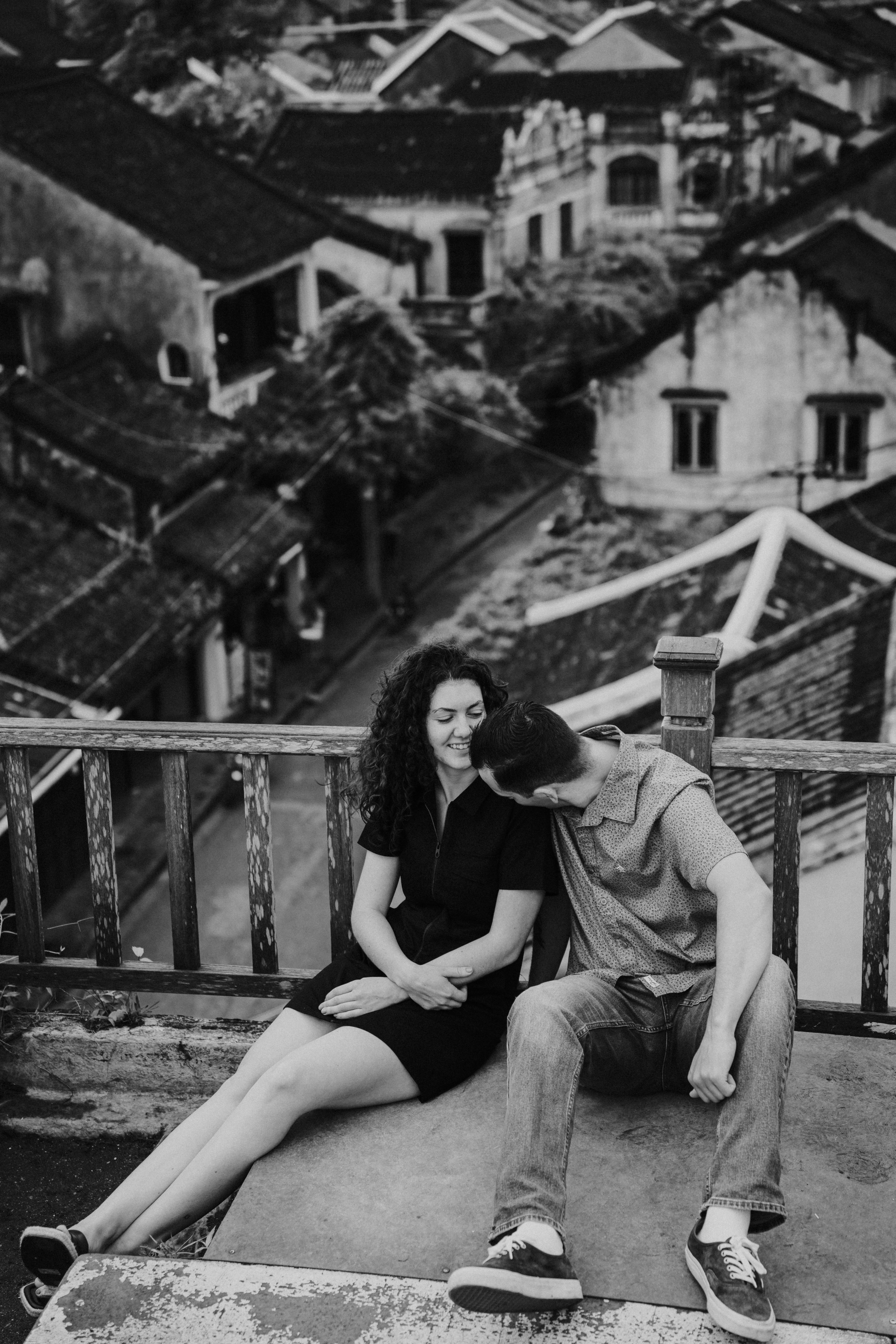 Couple on a rooftop ledge share a quiet moment against a hillside town backdrop