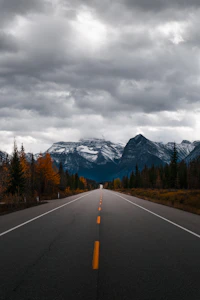 Open Road to Snow‑capped Peaks Under Brooding Sky