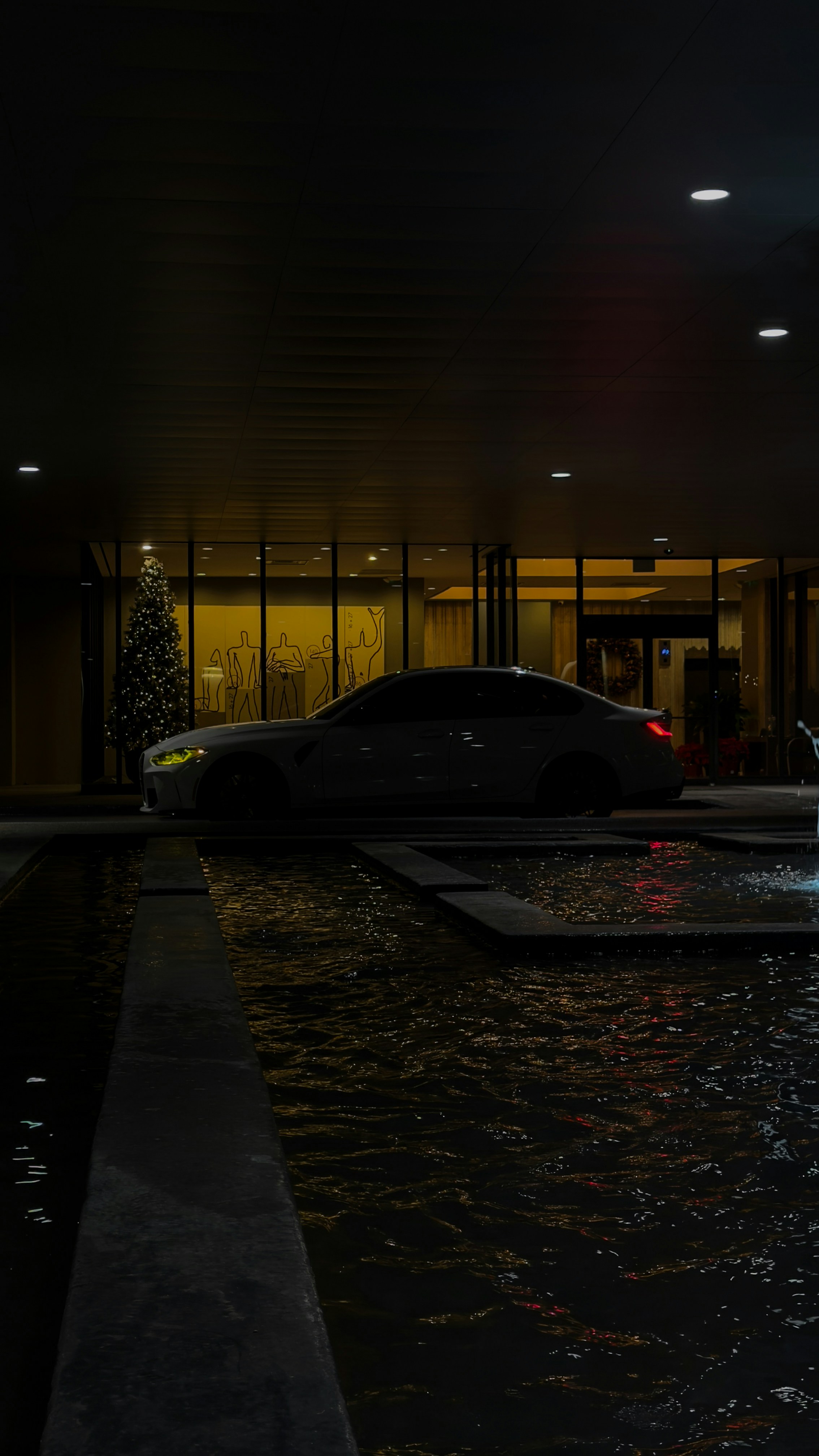 A white car parked by a water feature at night.