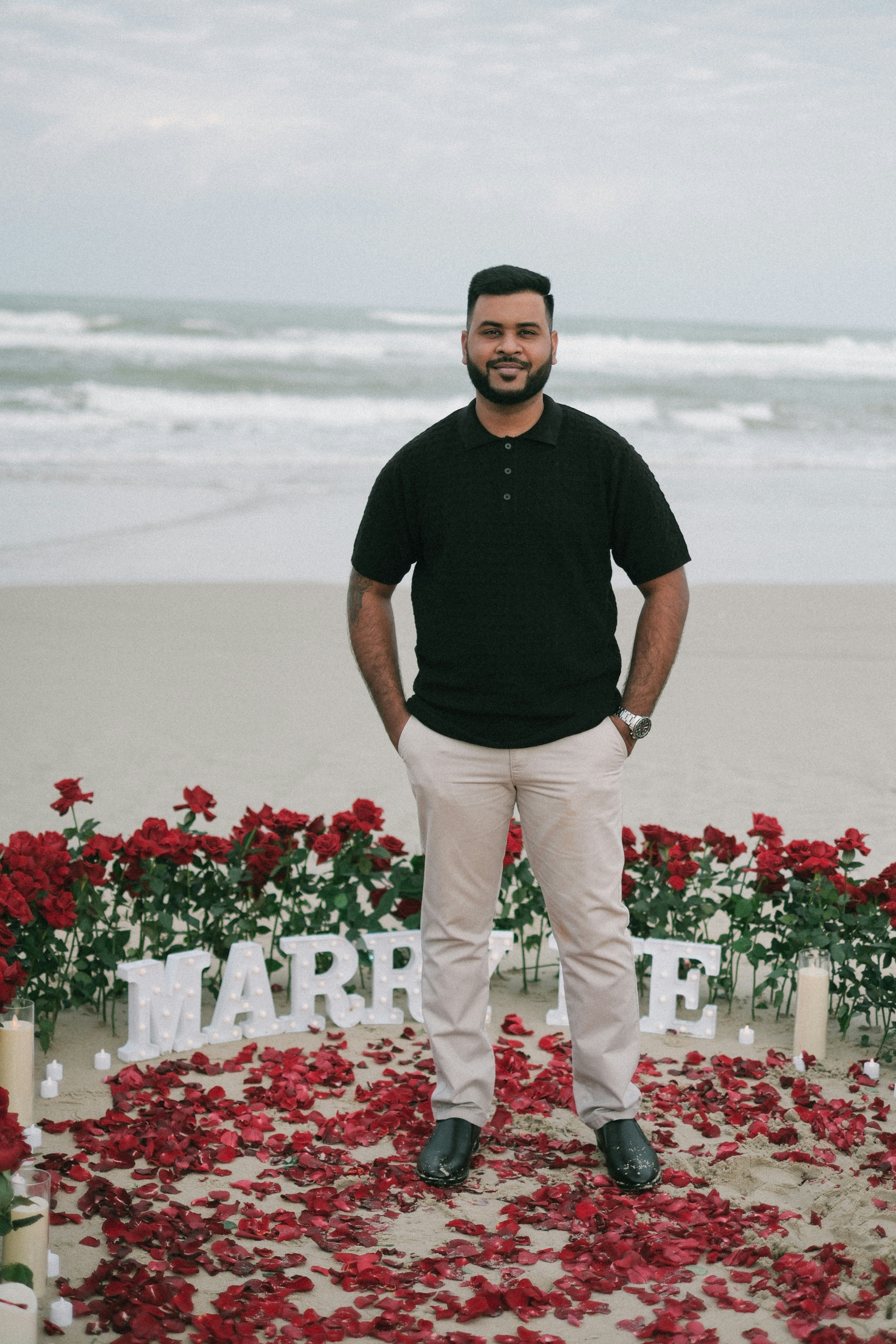 Coastal Groomed Confidence: A Man Stands Amid Red Bouquets by the Sea