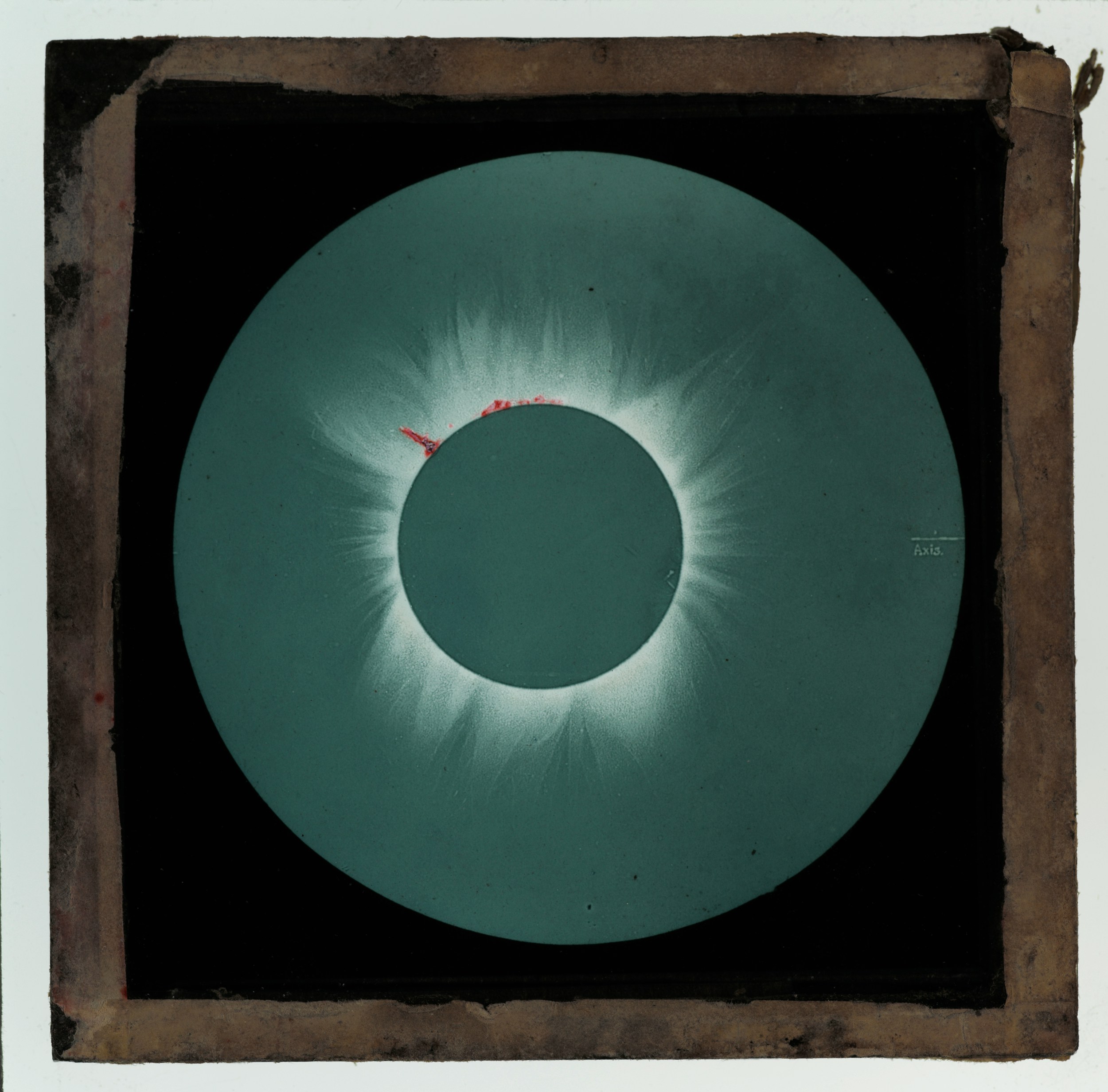 A lantern slide produced by Clement Lindley Wragge (b.1852, d.1922), dated 8 March 1909. The slide shows an image of a solar eclipse. The Sun is represented by a yellow/orange crescent with red/white cracks across surface. Placed across the lower section of the sun is a dark semi circle, representative of the moon. Shared by Auckland War Memorial Museum, Tāmaki Paenga Hira, as part of the Clement Lindley Wragge collection
