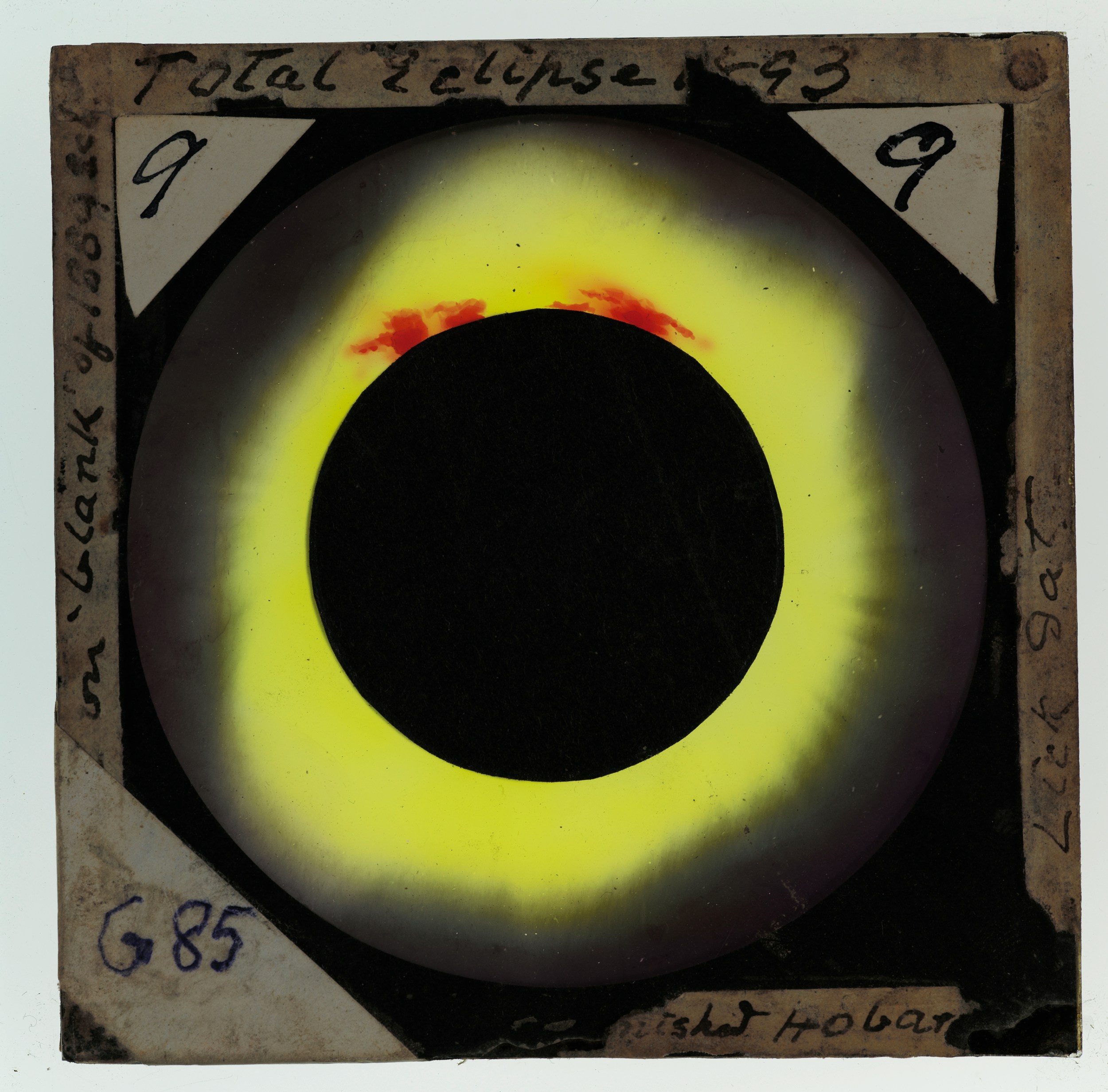 A dark central disk surrounded by a vivid yellow halo sits within a square frame marked with handwritten annotations, suggesting an experimental eclipse study; the image is a photographic print or negative simulation.