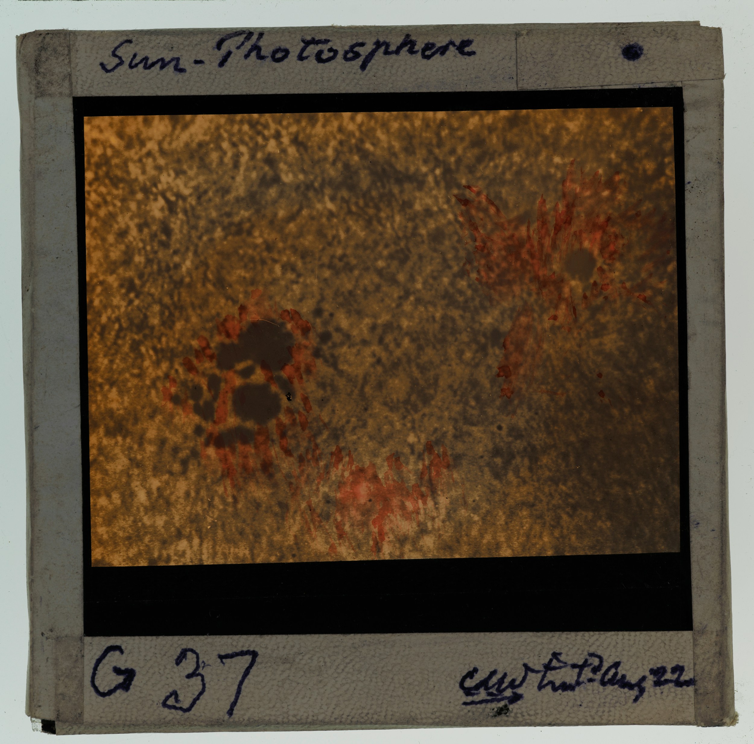 A lantern slide produced by Clement Lindley Wragge (b.1852, d.1922), likely dating between 1890-1922. The slide is an orange/red tinted plate, depicting an image of dark masses on the surface of the sun. Shared by Auckland War Memorial Museum, Tāmaki Paenga Hira, as part of the Clement Lindley Wragge collection. 235958|PH-1984-1-LS78-3-29|37. No known copyright restrictions. https://www.aucklandmuseum.com/discover/collections/record/1033257