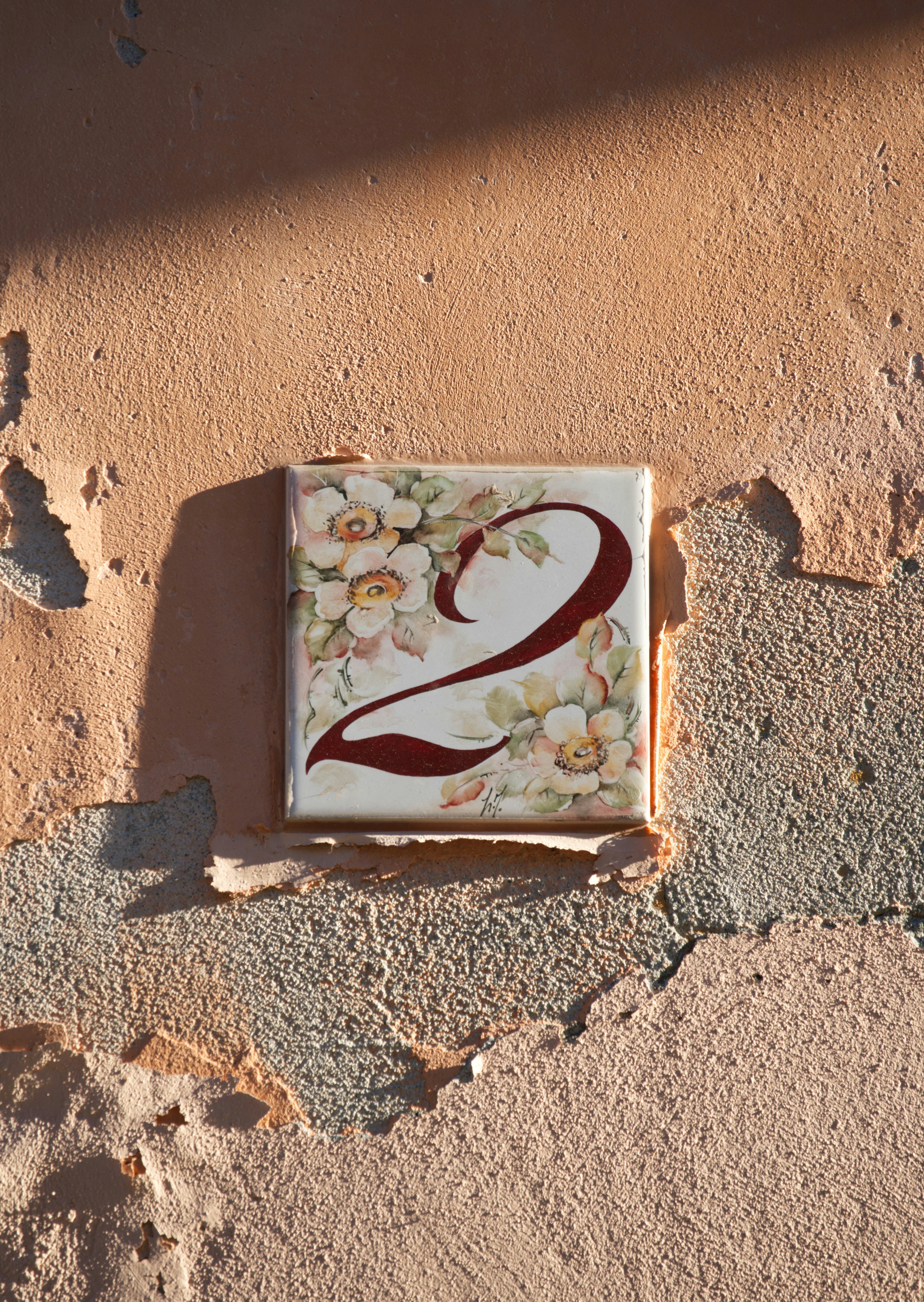 Tile with a Scarlet Swoop: A Flowered Number on Weathered Stucco