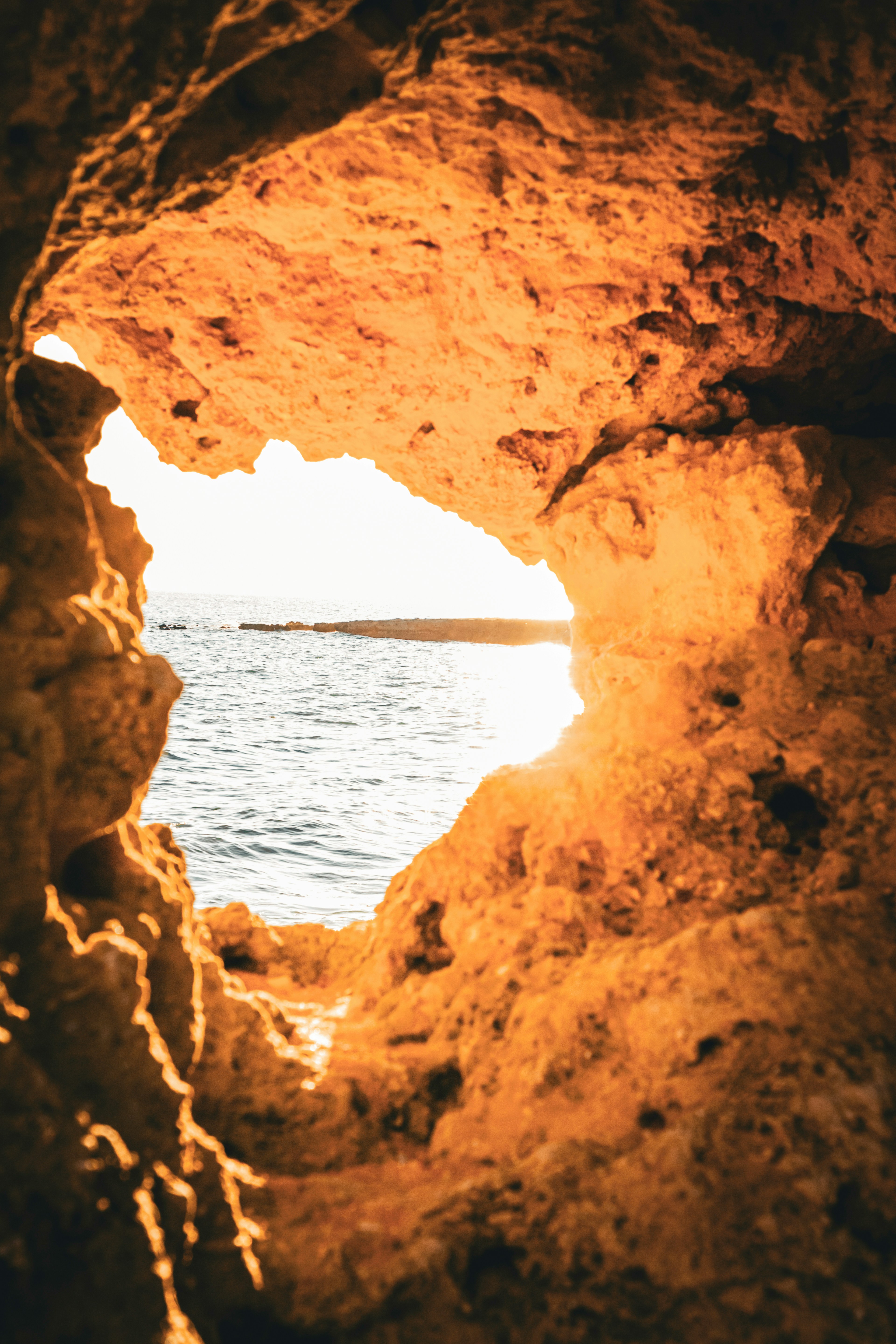 Warm sunlight illuminates a rugged coastal cave in Portugal at sunset. Natural rock formations frame the calm ocean waters. Scenic seascape with golden light and textured cliffs.
