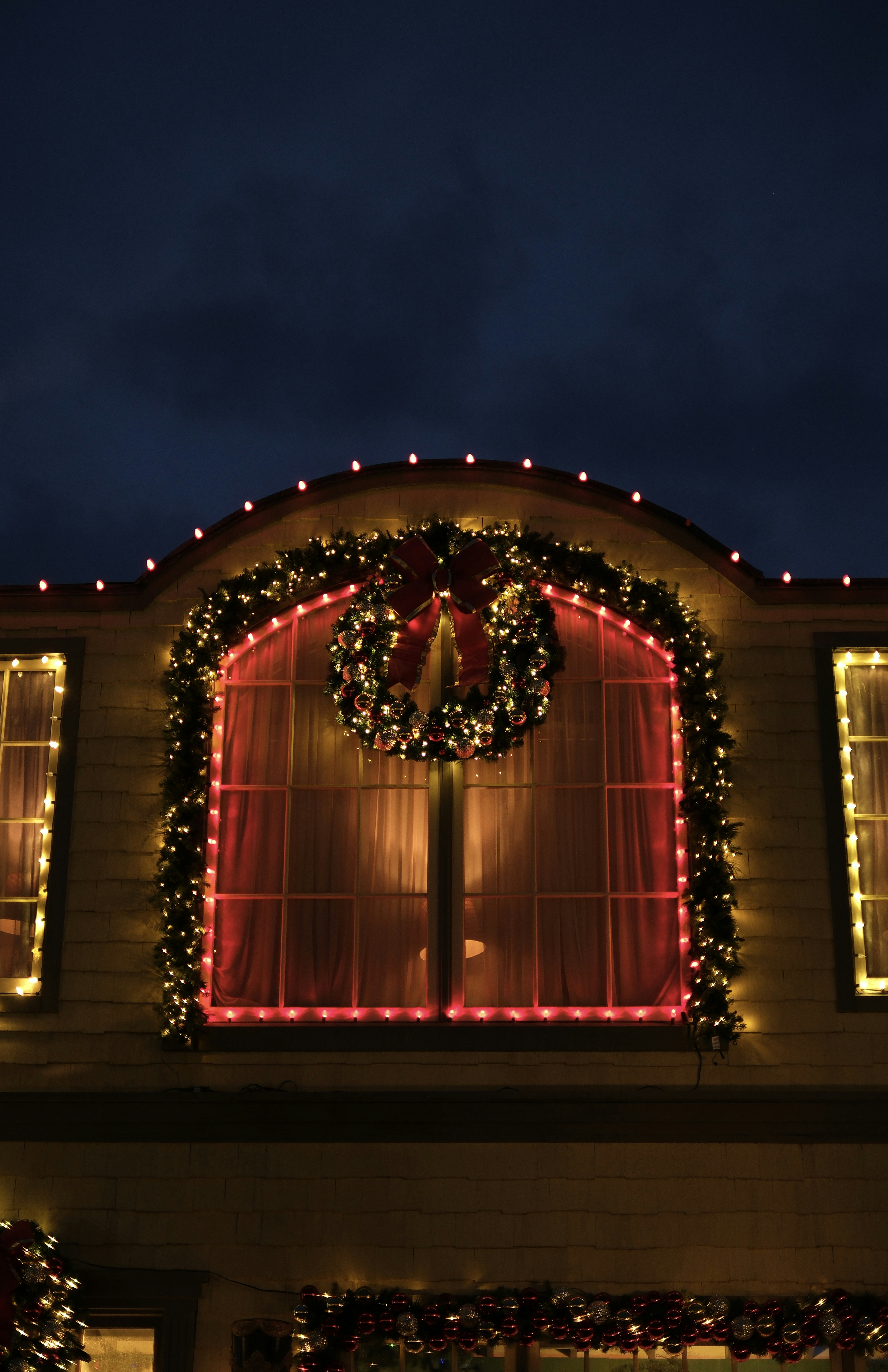Festive Window: Warm Glow of Holiday Lights in a Garlanded Facade