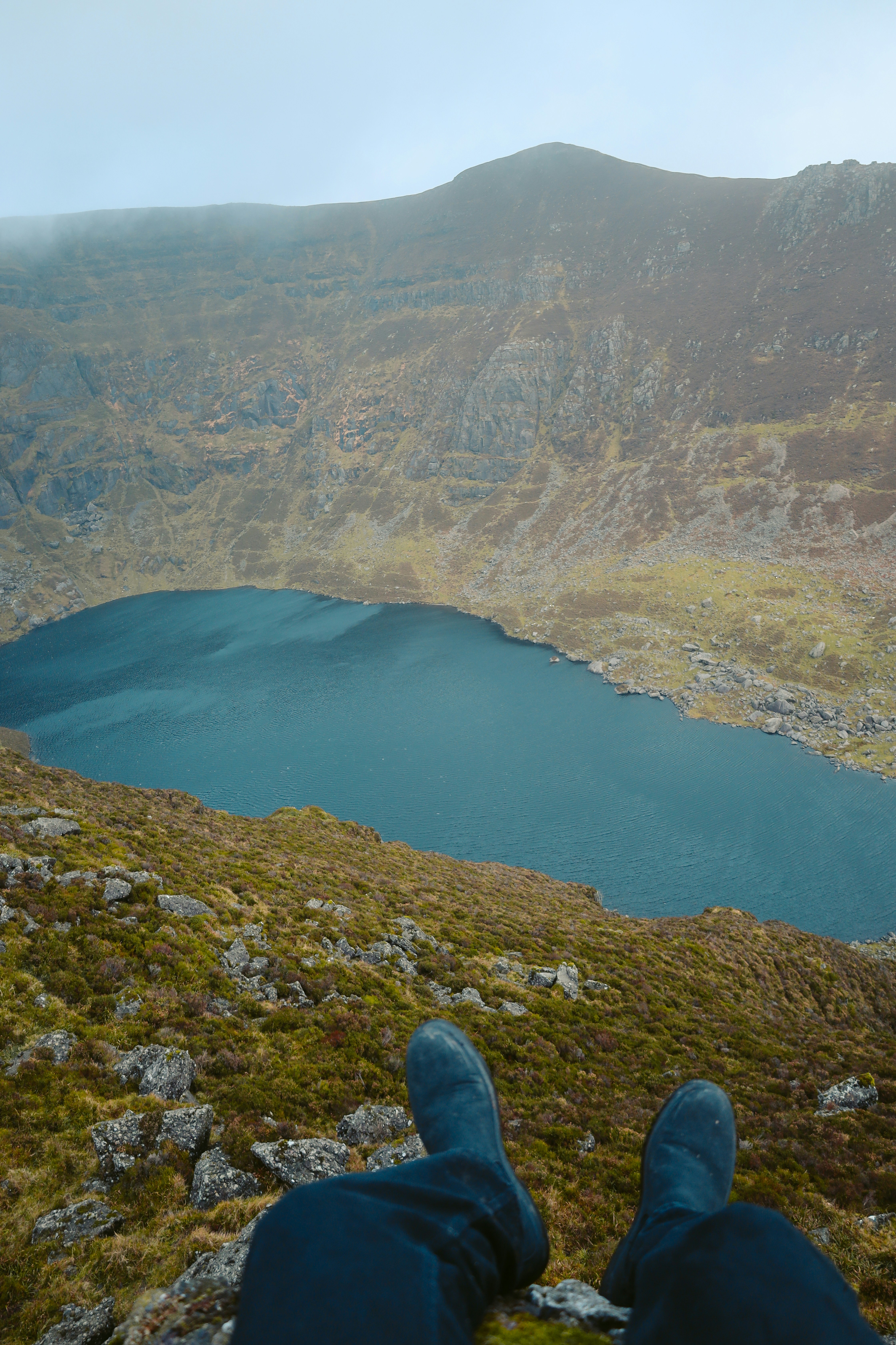 Over the Edge: Boots at the Rim Above a Quiet Crater Lake