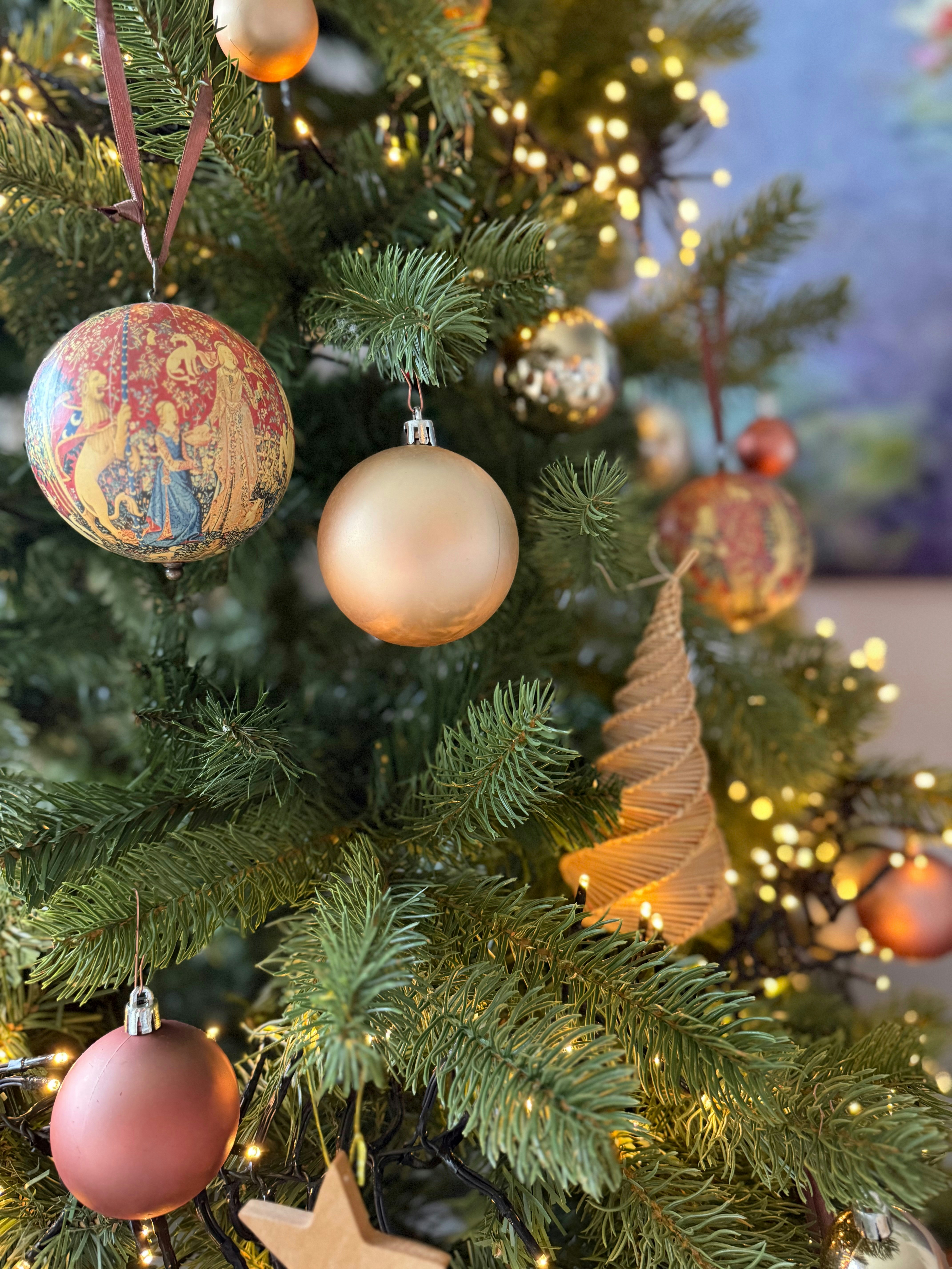 Christmas ornaments on a decorated Christmas tree. The main ornament displays a design inspired by the medieval Flemish tapestries known as ‘The Lady and the Unicorn’ (French: La Dame à la licorne), which symbolically represents ‘taste’ and ‘smell’ in the mille-fleurs style. This artwork is housed at the Musée de Cluny in Paris, France.