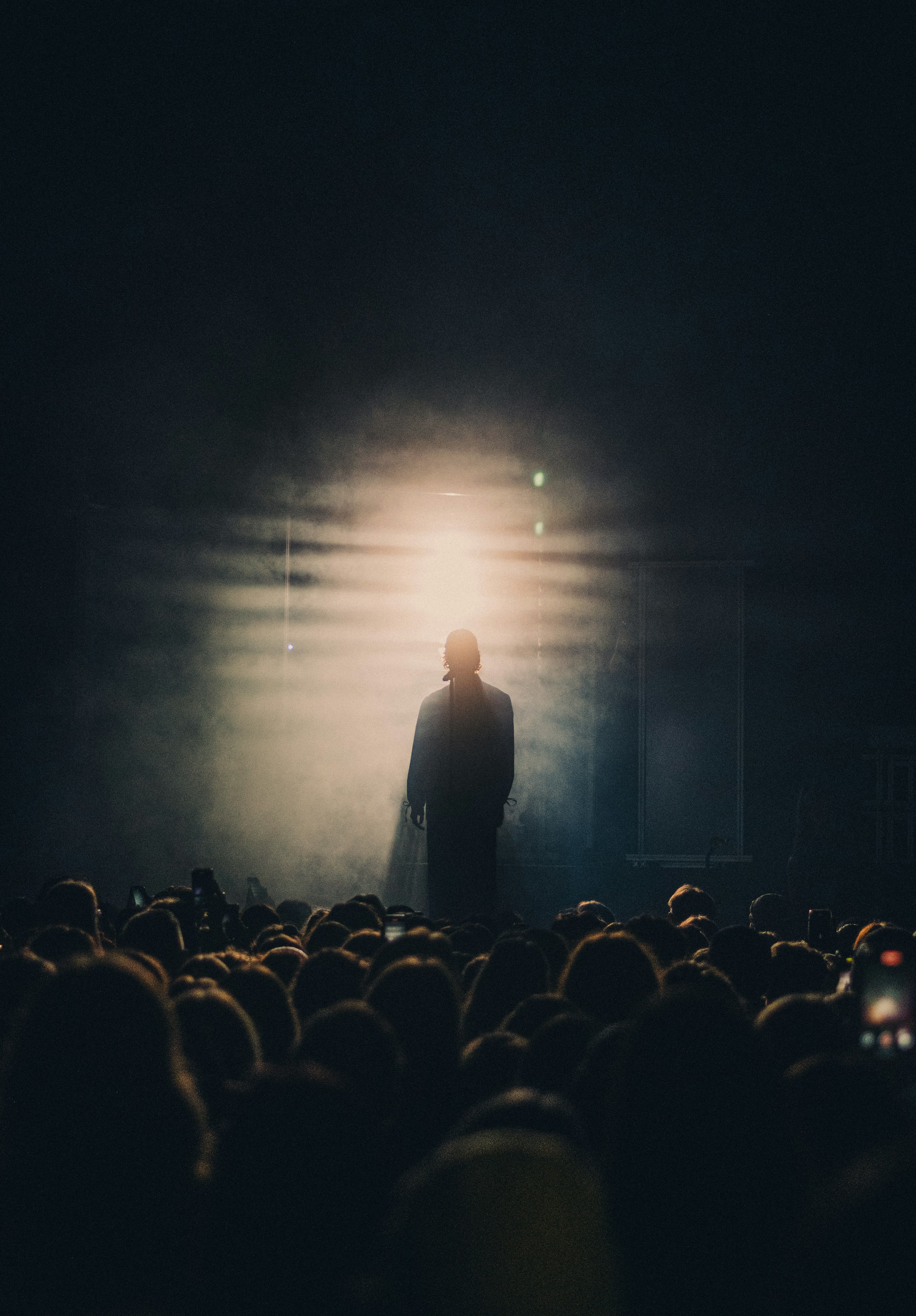 Backlit silhouette at center stage: a lone performer in fog and light
