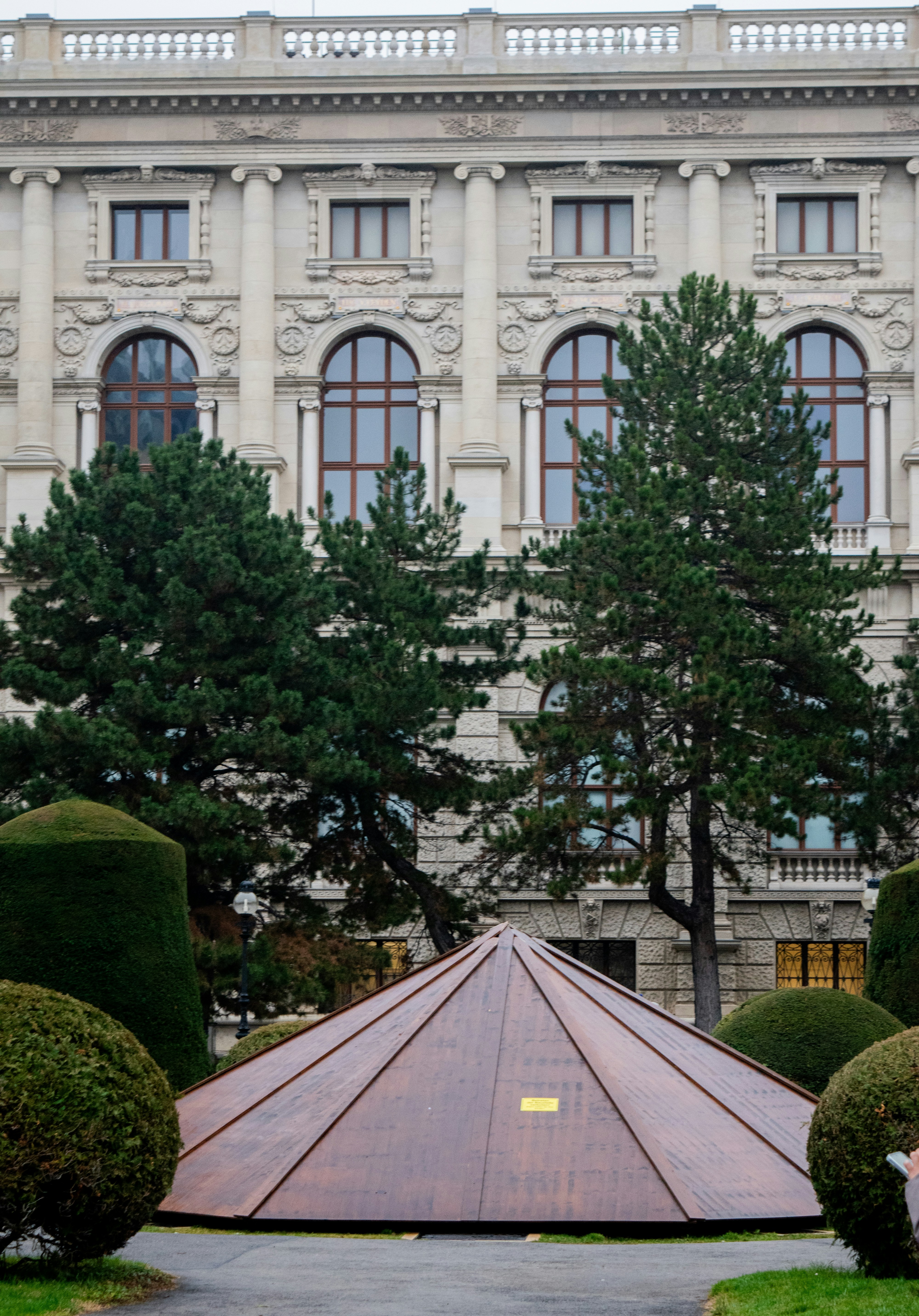 Tree-lined courtyard with copper-topped pavilion in front of ornate stone facade