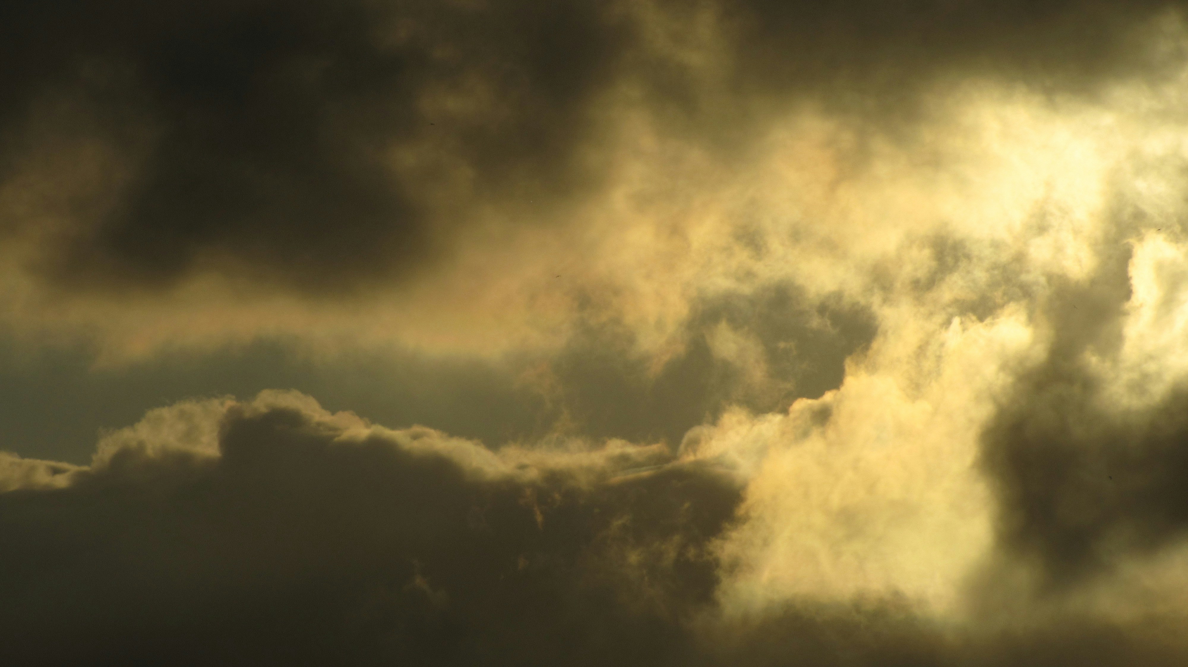 A peaceful yet dramatic moment as warm sunlight breaks through a layer of dense, dark clouds. The glowing haze adds depth and texture, capturing the quiet beauty of a changing sky.