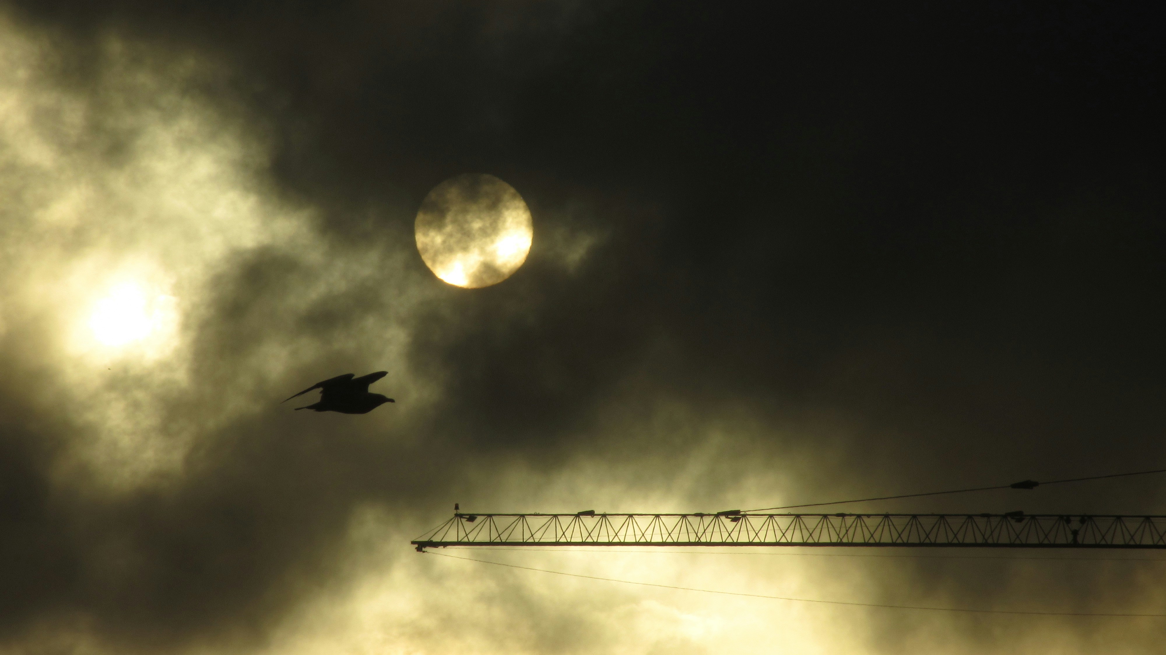 Dark storm clouds drift across a sky glowing with golden light, creating a dramatic contrast between shadow and warmth.