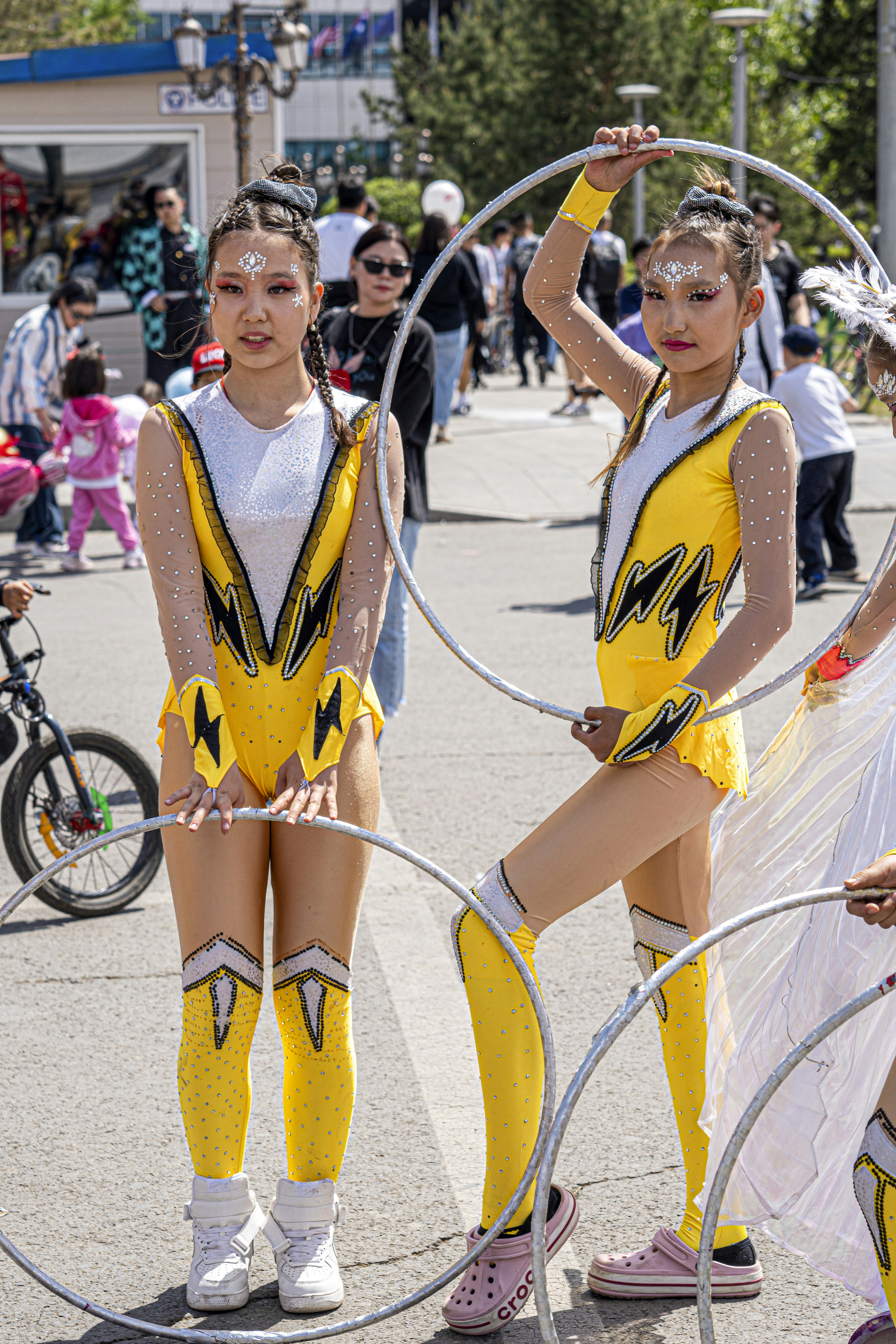 Two young circus performers standing confidently in vibrant costumes during an outdoor cultural parade.