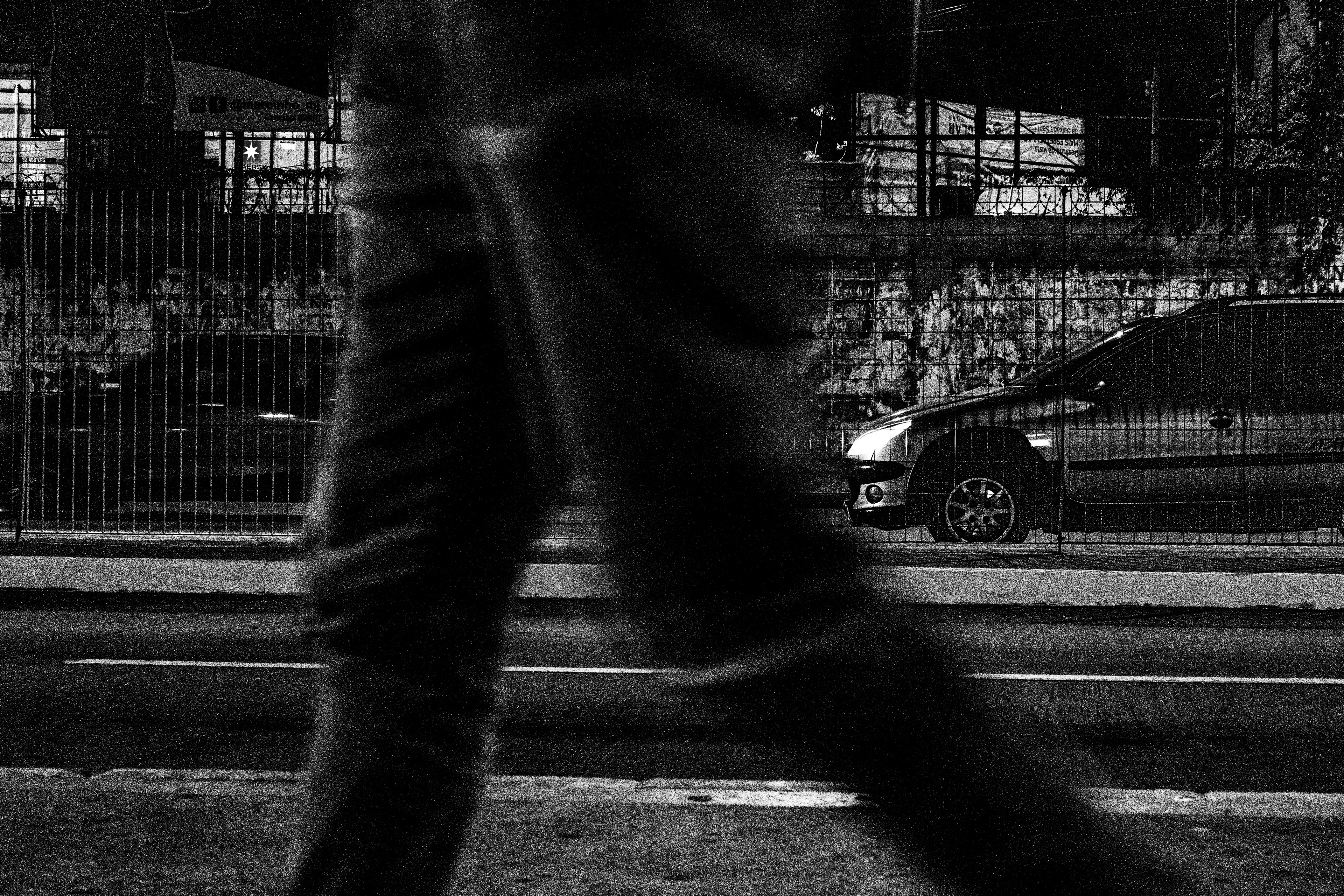 A person walks past a parked car on a street at night.
