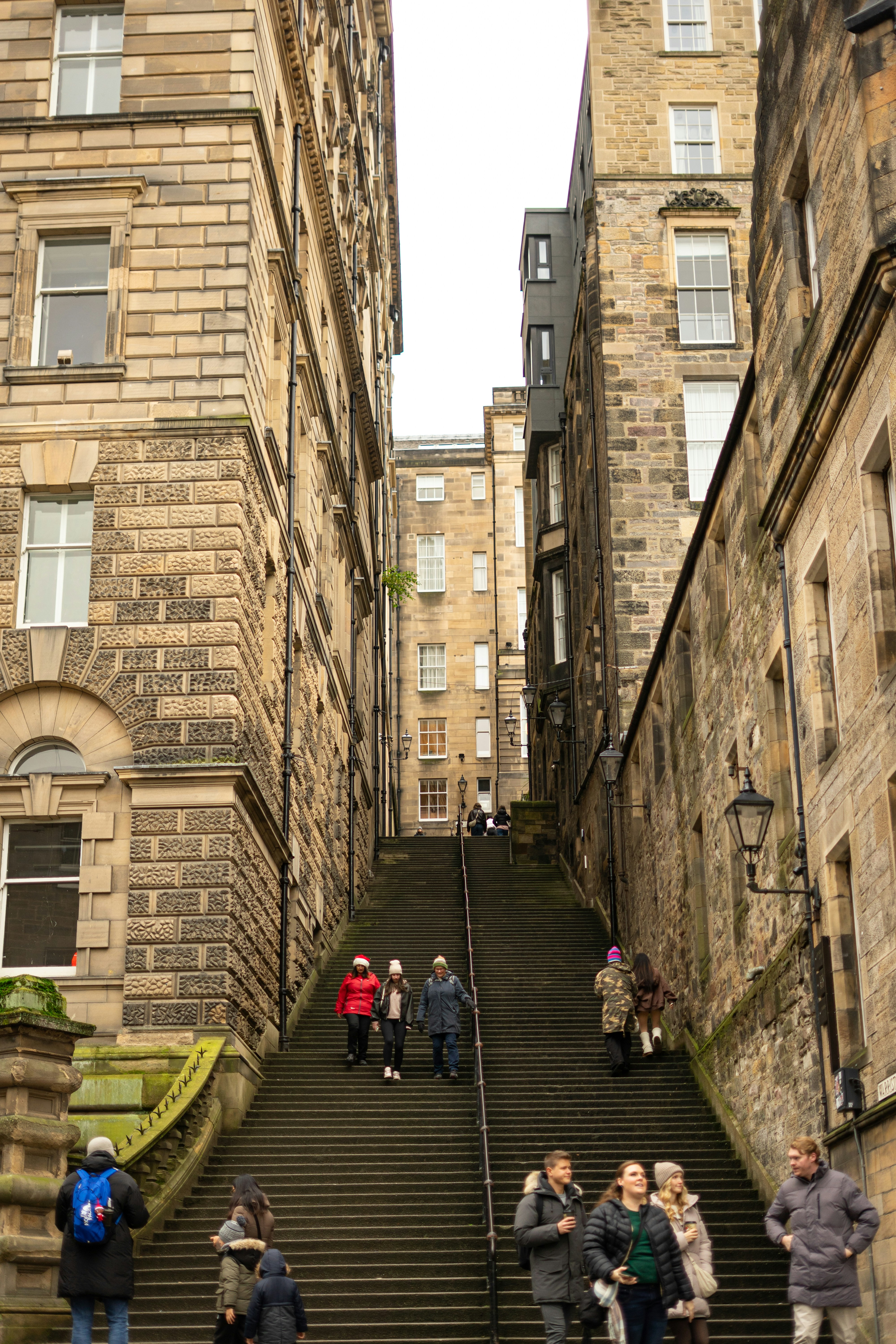 People ascend a steep stone staircase between old buildings. photo ...